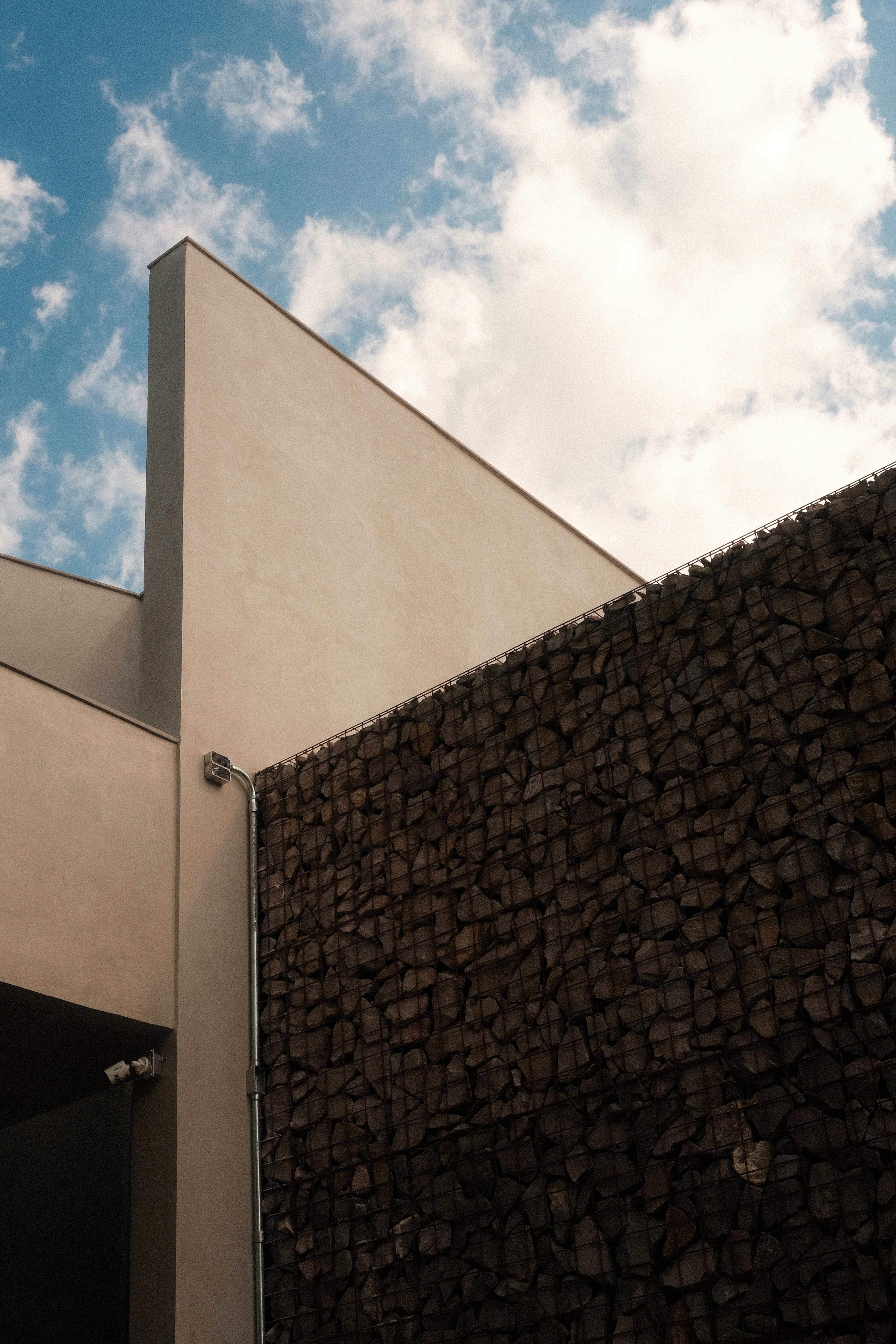 Angular architecture with textured stone wall against a backdrop of clouds and blue sky.