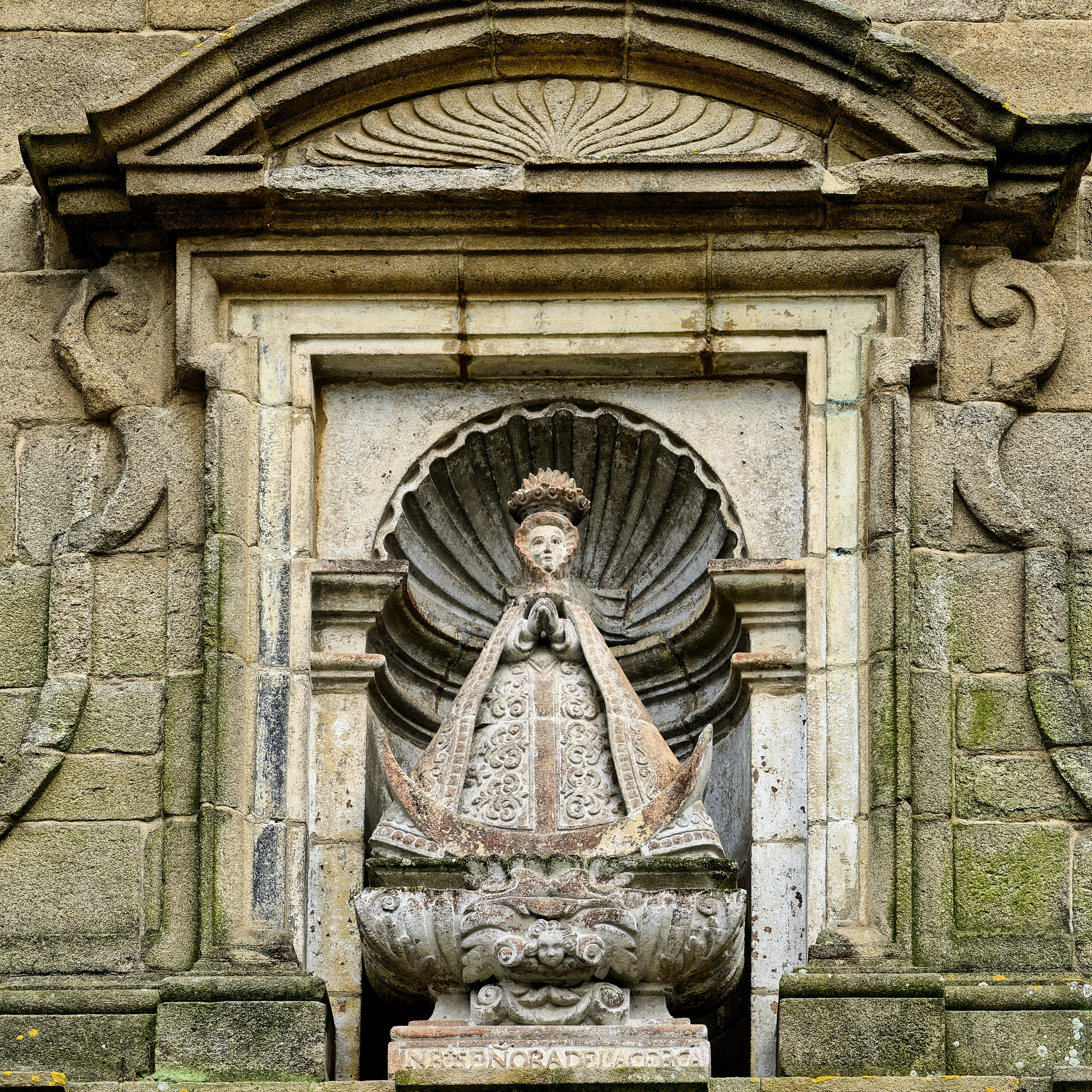 Intricate stone sculpture of a serene saint set in an ornate church wall alcove.