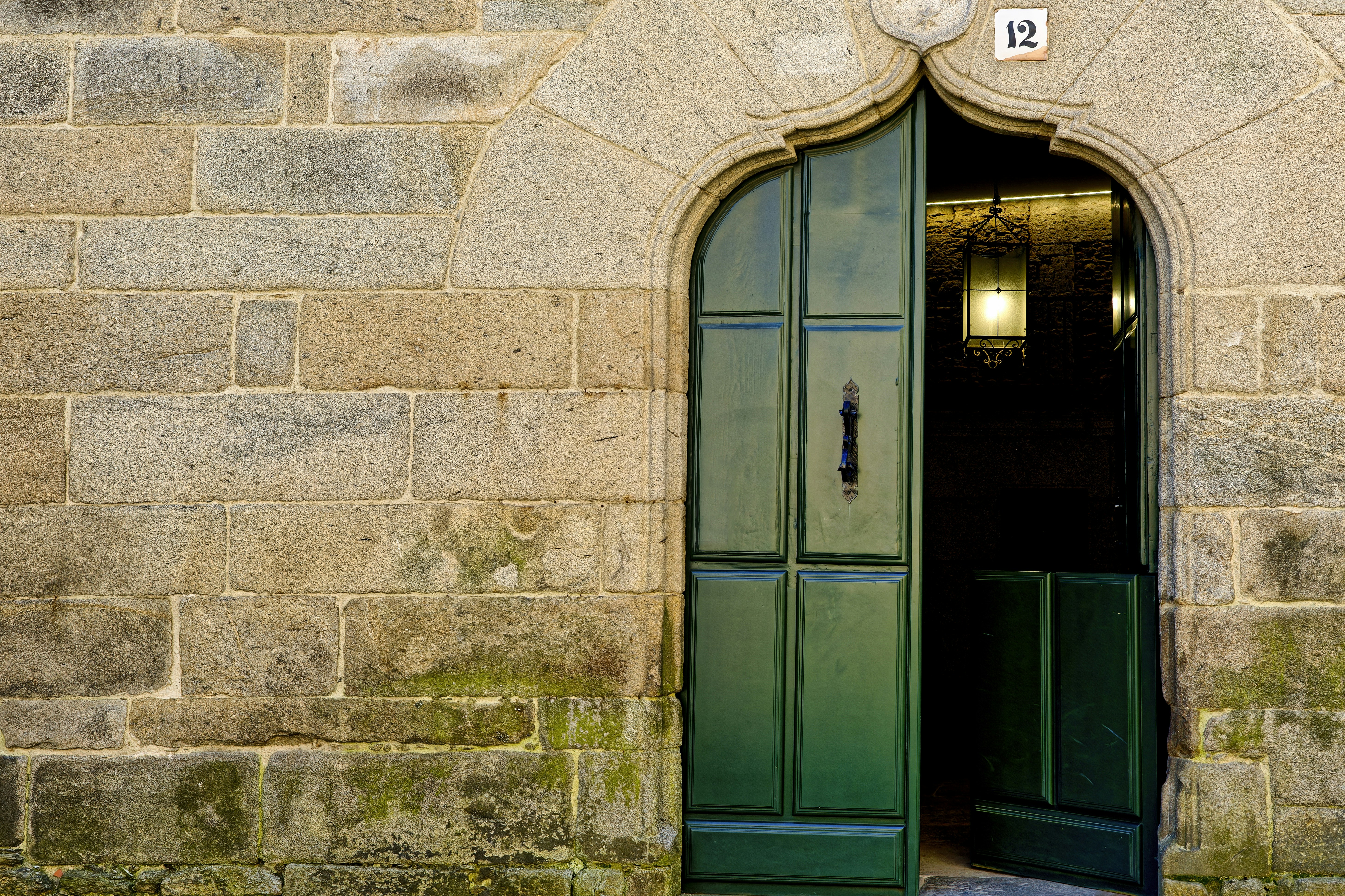 Green door set in a stone archway, slightly open with warm interior light visible.