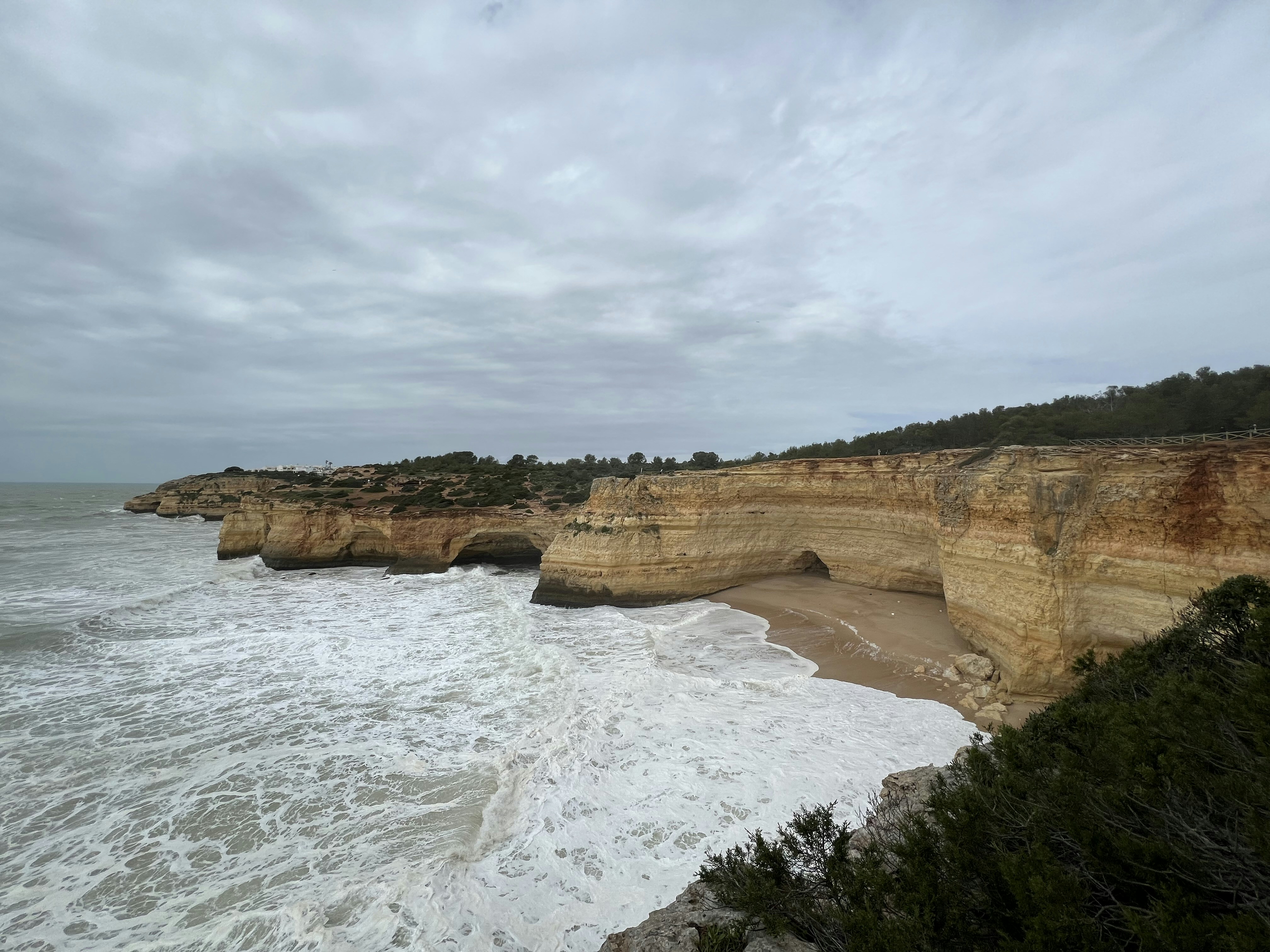 Rugged cliffs overlooking a turbulent sea under a cloudy sky.