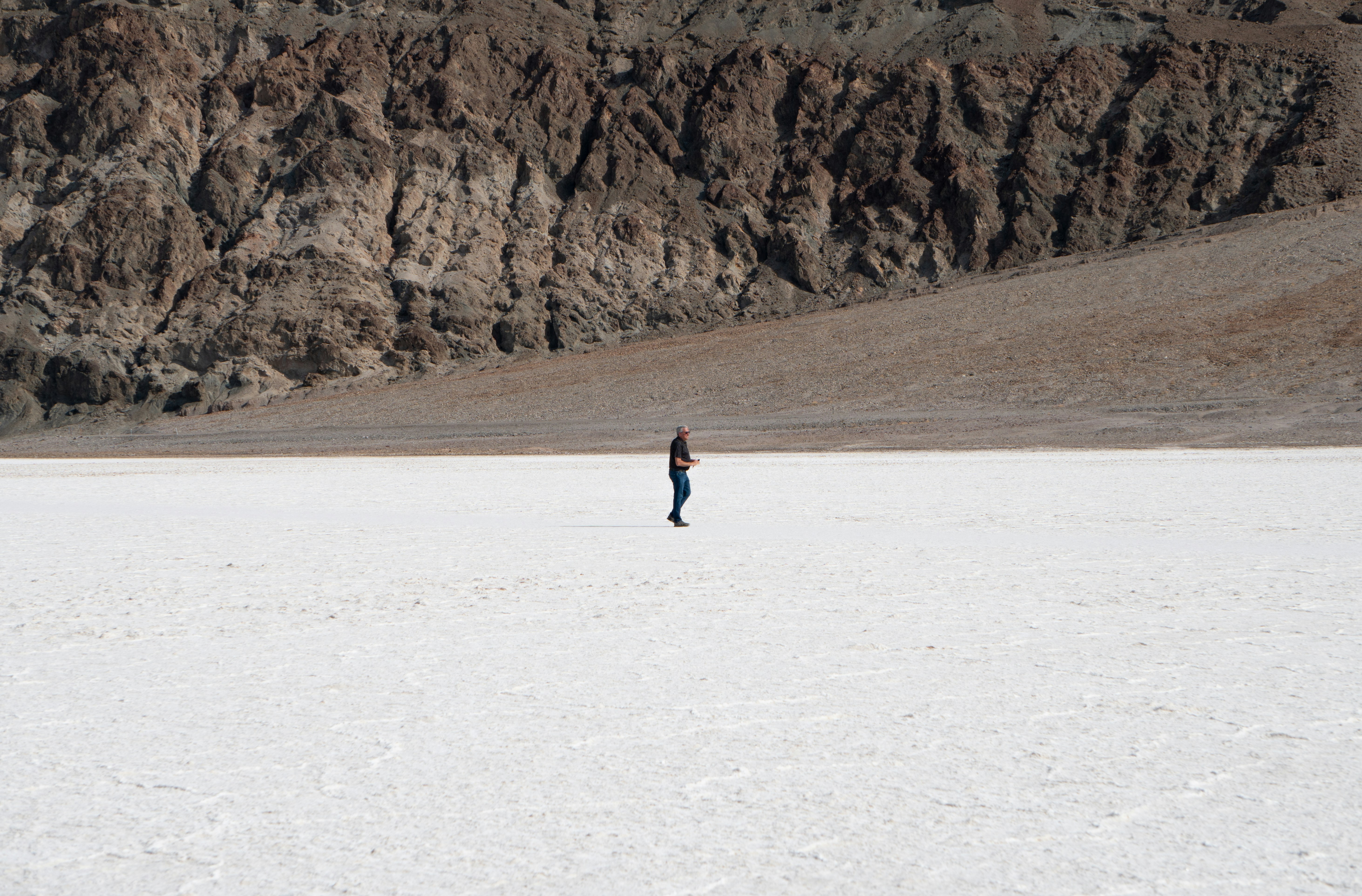A lone figure traversing the expansive, white salt flats with rugged mountains in the background.