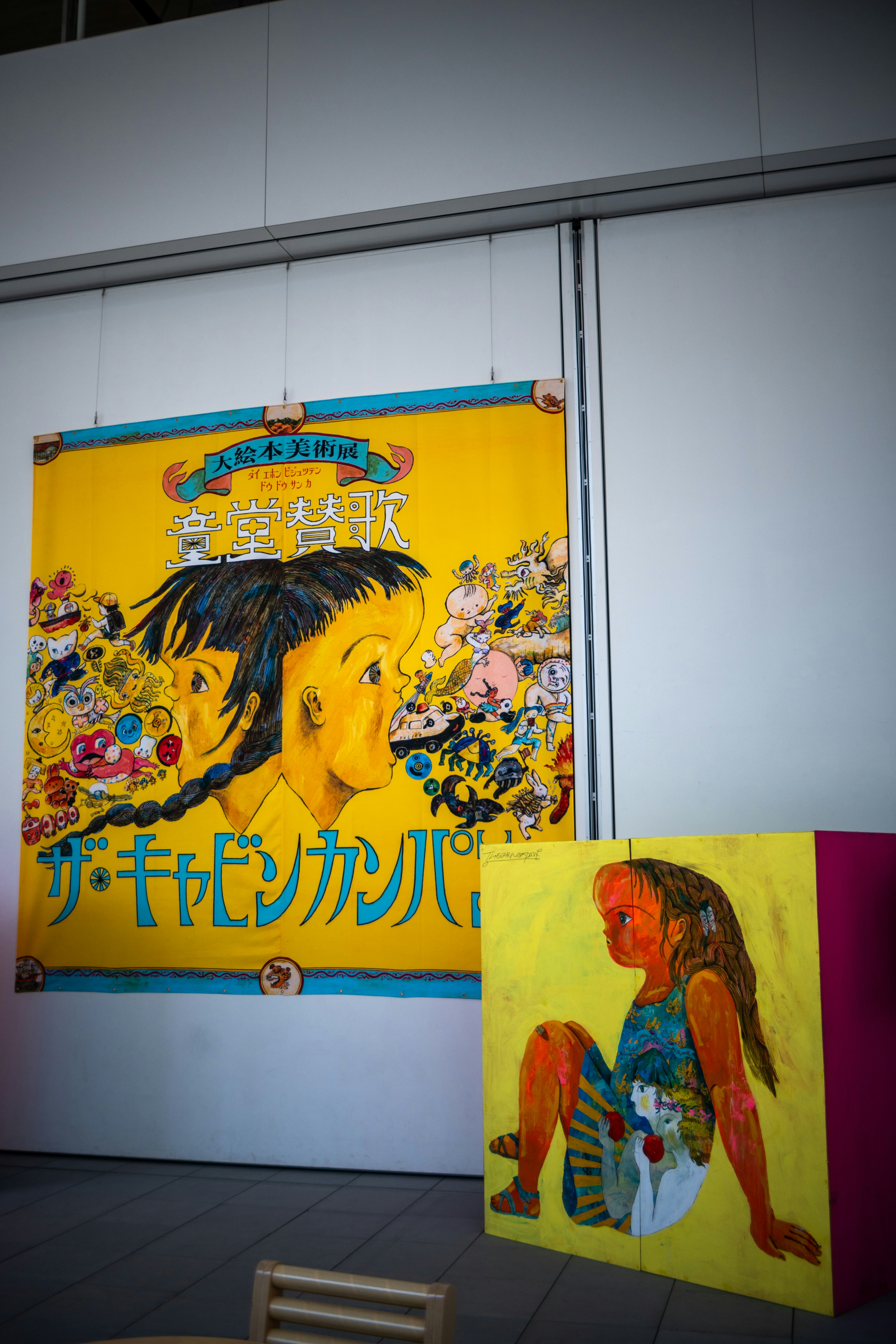 Vibrant mural featuring playful characters and two stylized faces, accompanied by a bold illustration of a girl sitting against a yellow backdrop.