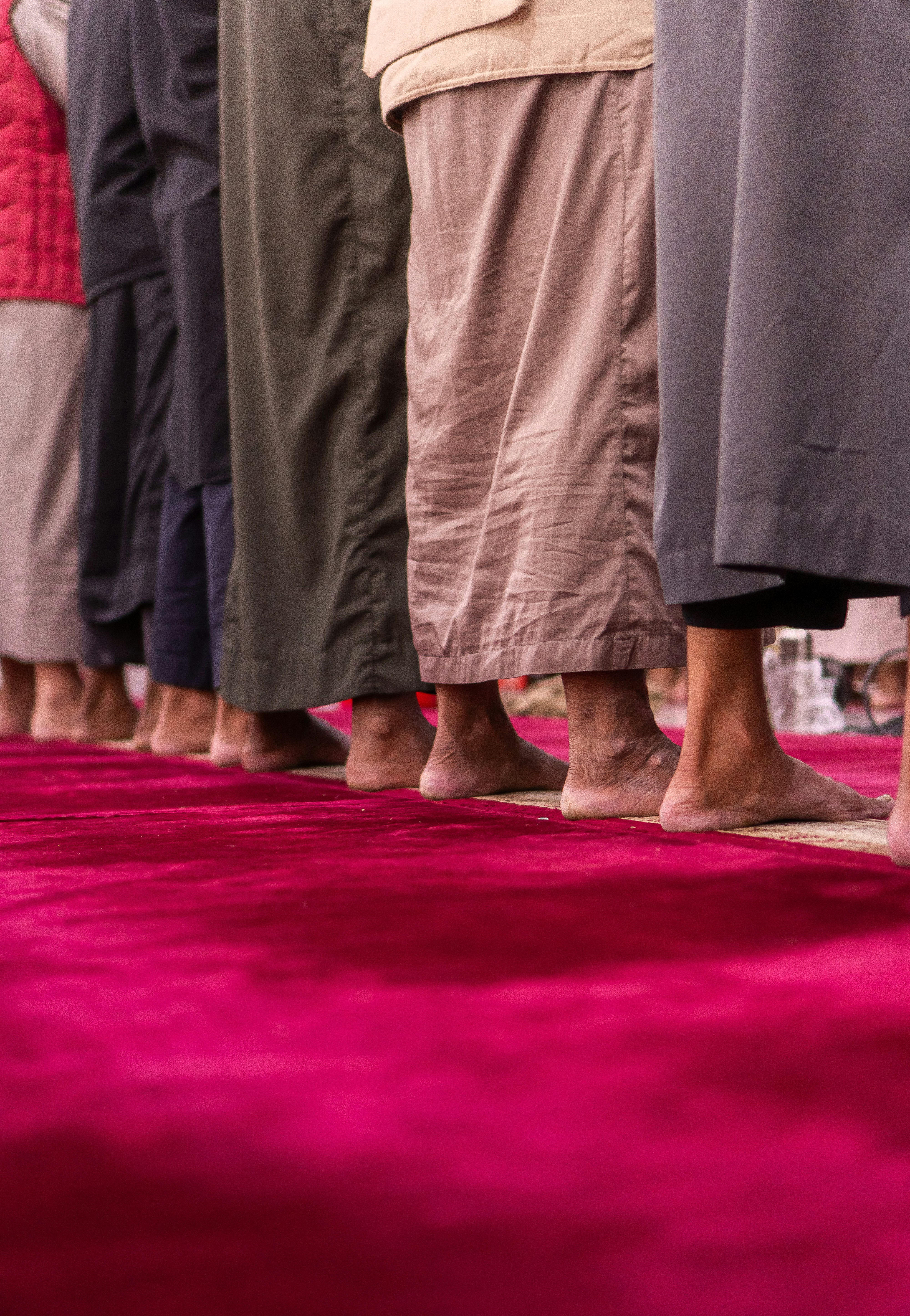 Men pray in a mosque, standing on a rug.