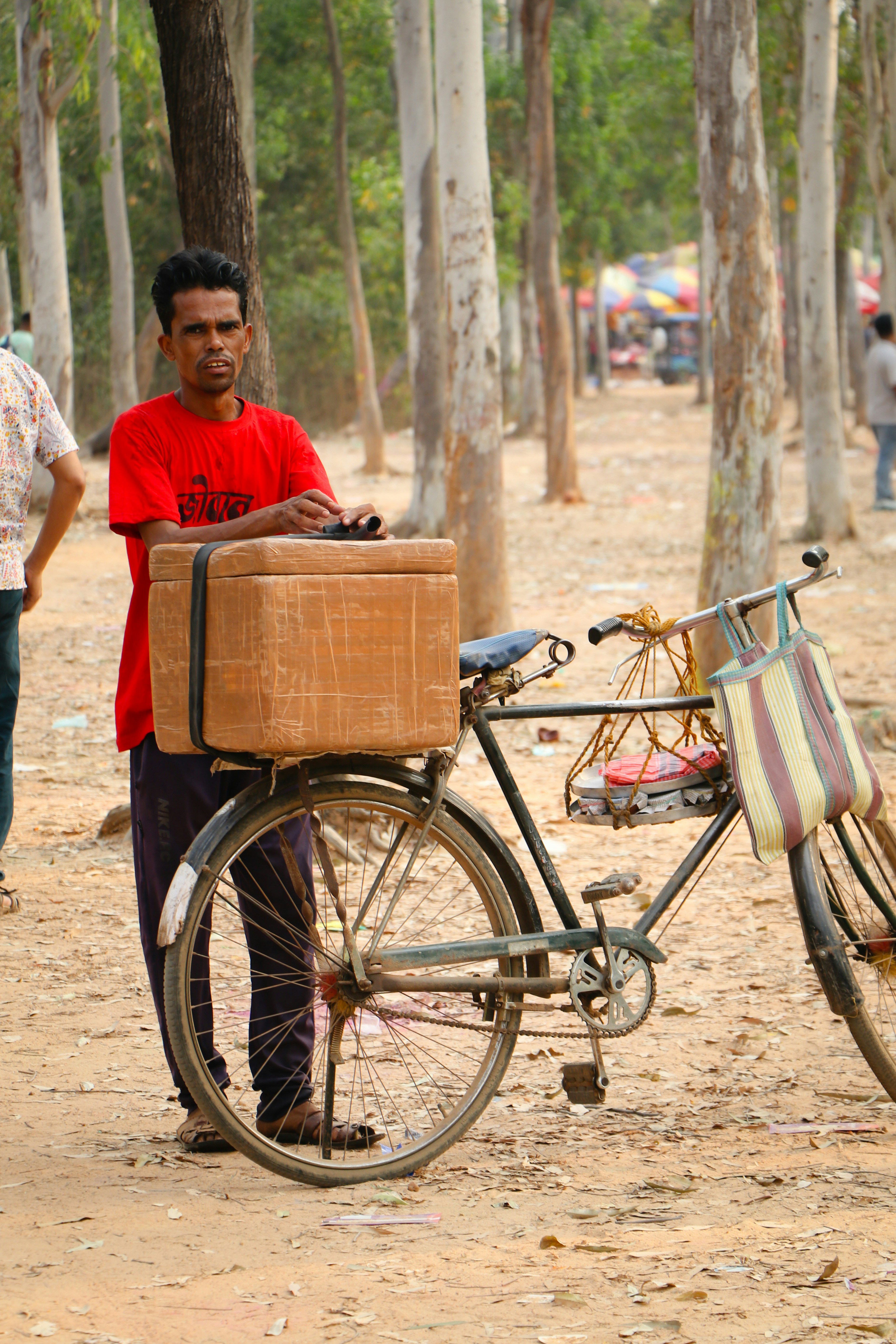 Cargo on Two Wheels: A Red-Shirt Courier with a Weathered Box by a Dusty Path