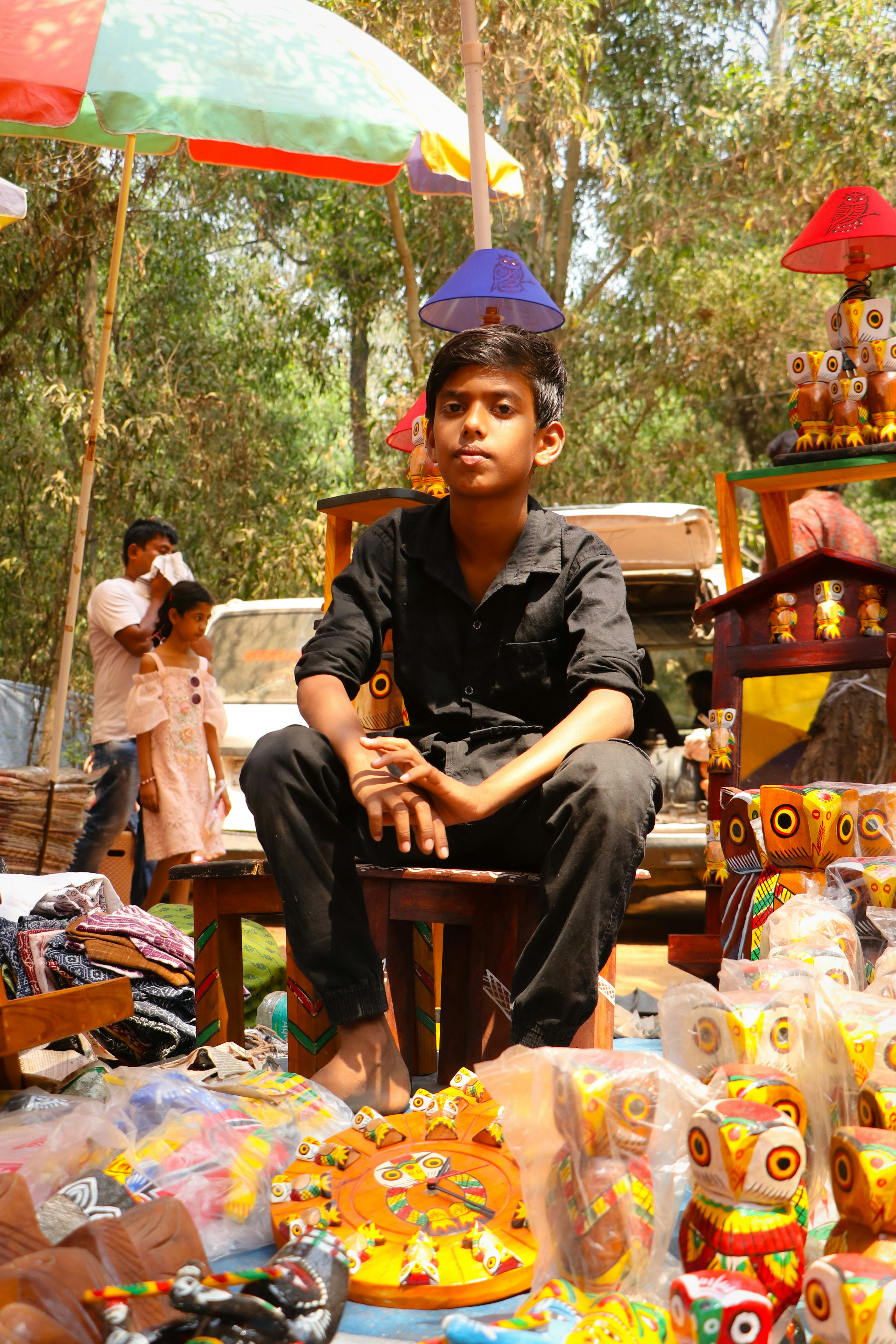 Central Boy Amid Handcrafted Owl Figurines in a Sunlit Market Stall