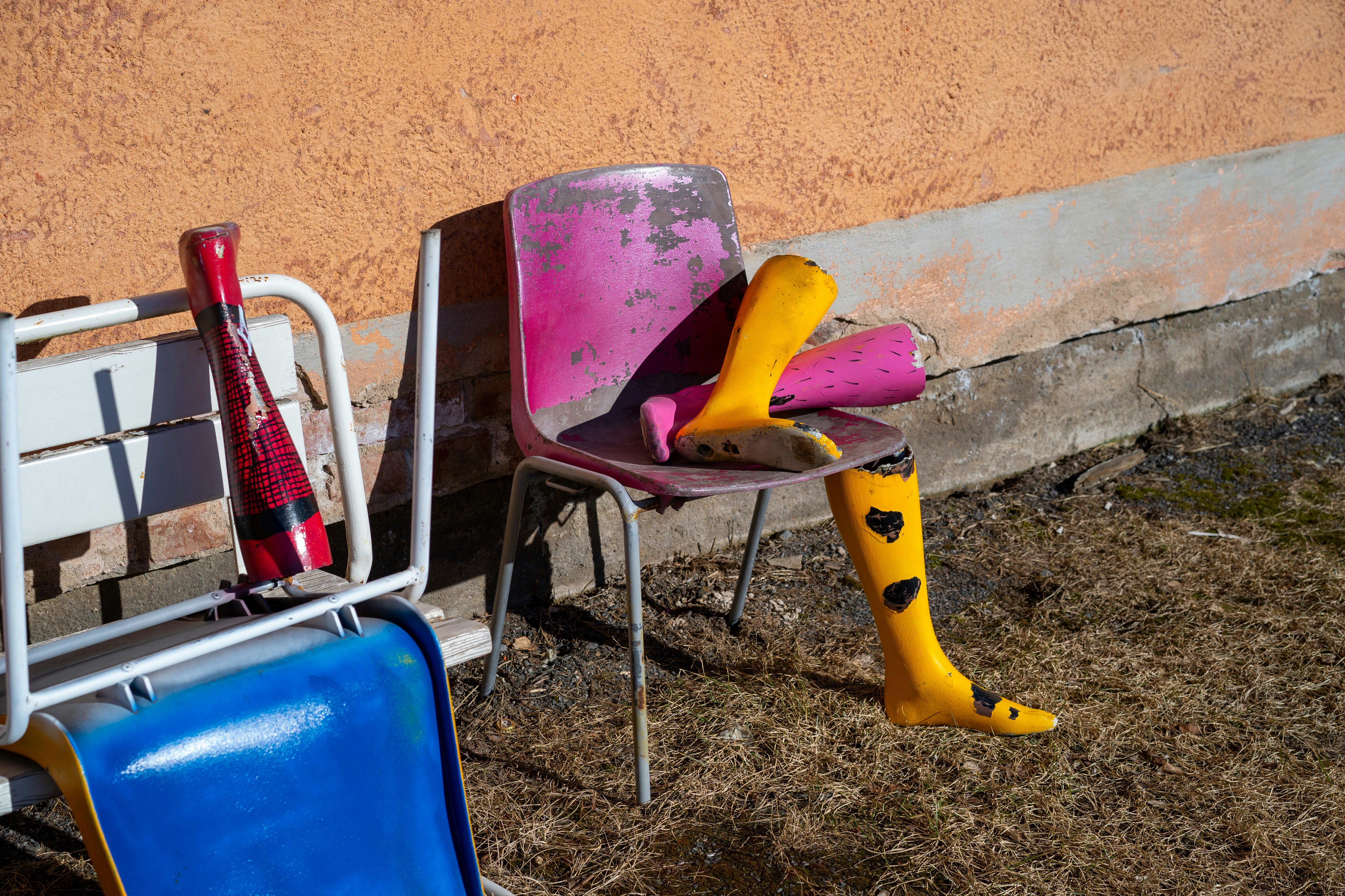 Sunlit Surreal: Yellow Leg on a Pink Chair Among Weathered Outdoor Furniture