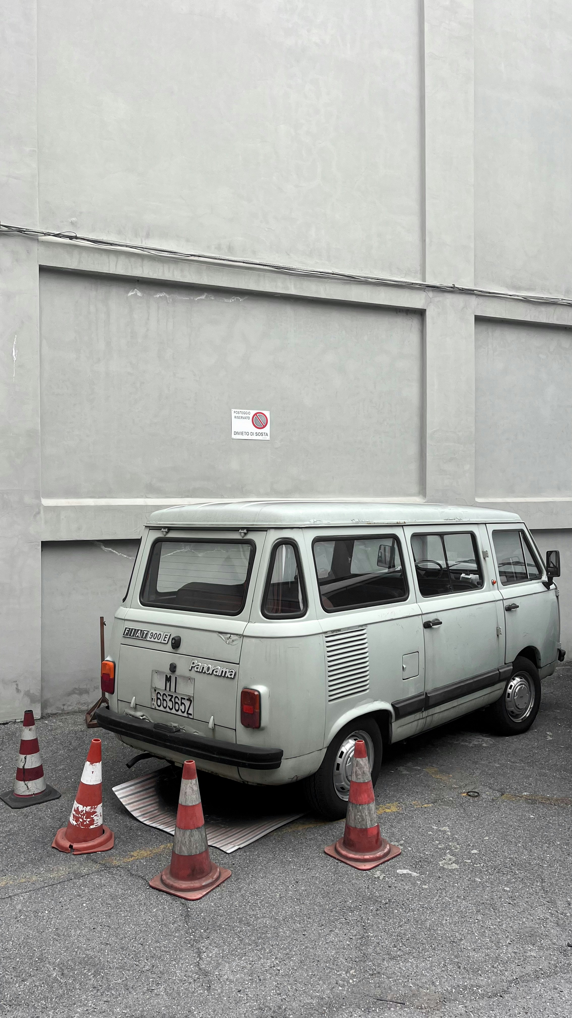 Vintage van parked between traffic cones against a stark concrete wall.