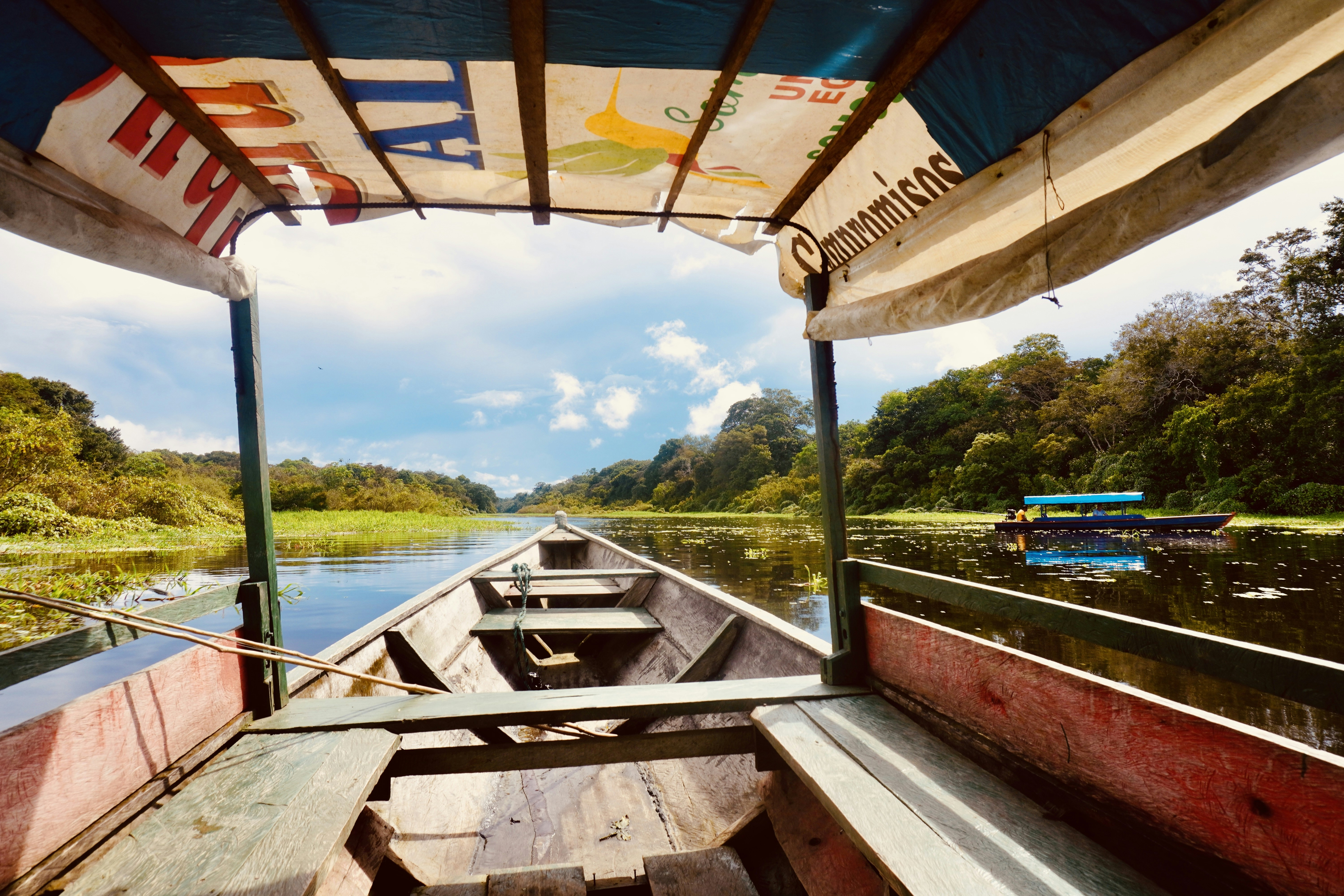 Wooden boat navigates a serene river surrounded by lush greenery under a partly cloudy sky.
