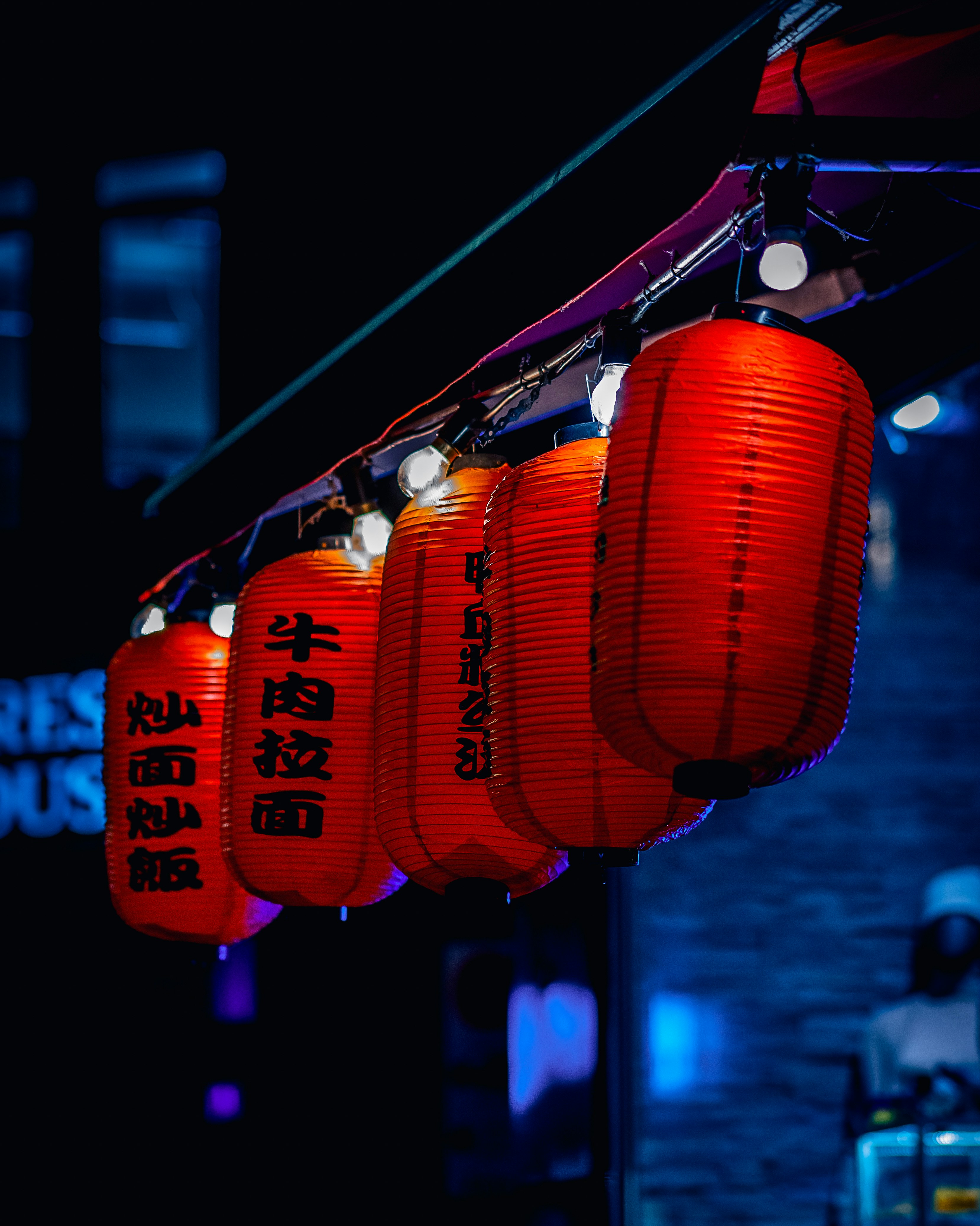 A row of vibrant red lanterns hangs against a dark backdrop, each adorned with intricate calligraphy, illuminating the night market ambiance.