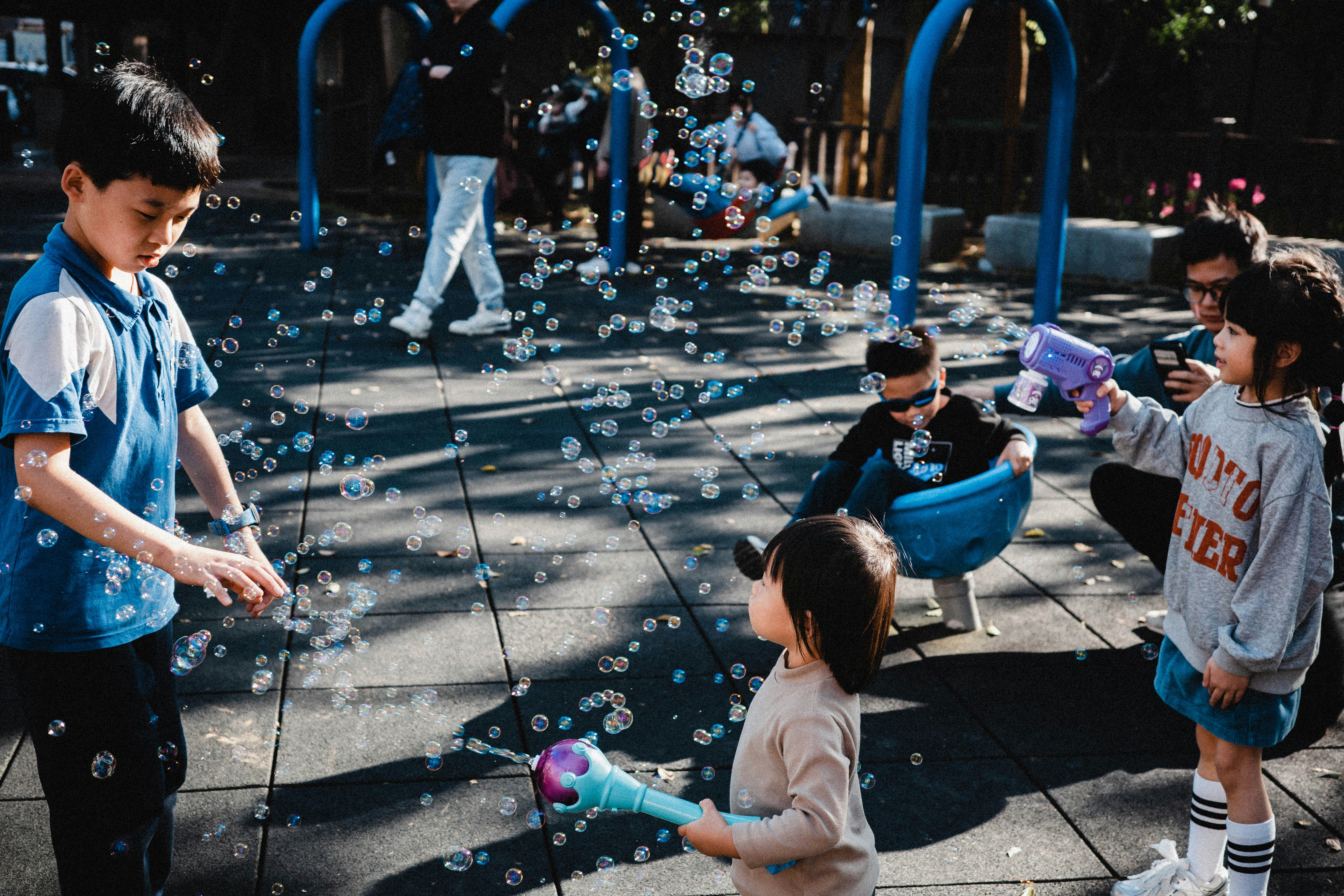 Children playing with bubbles in a sunny playground setting.