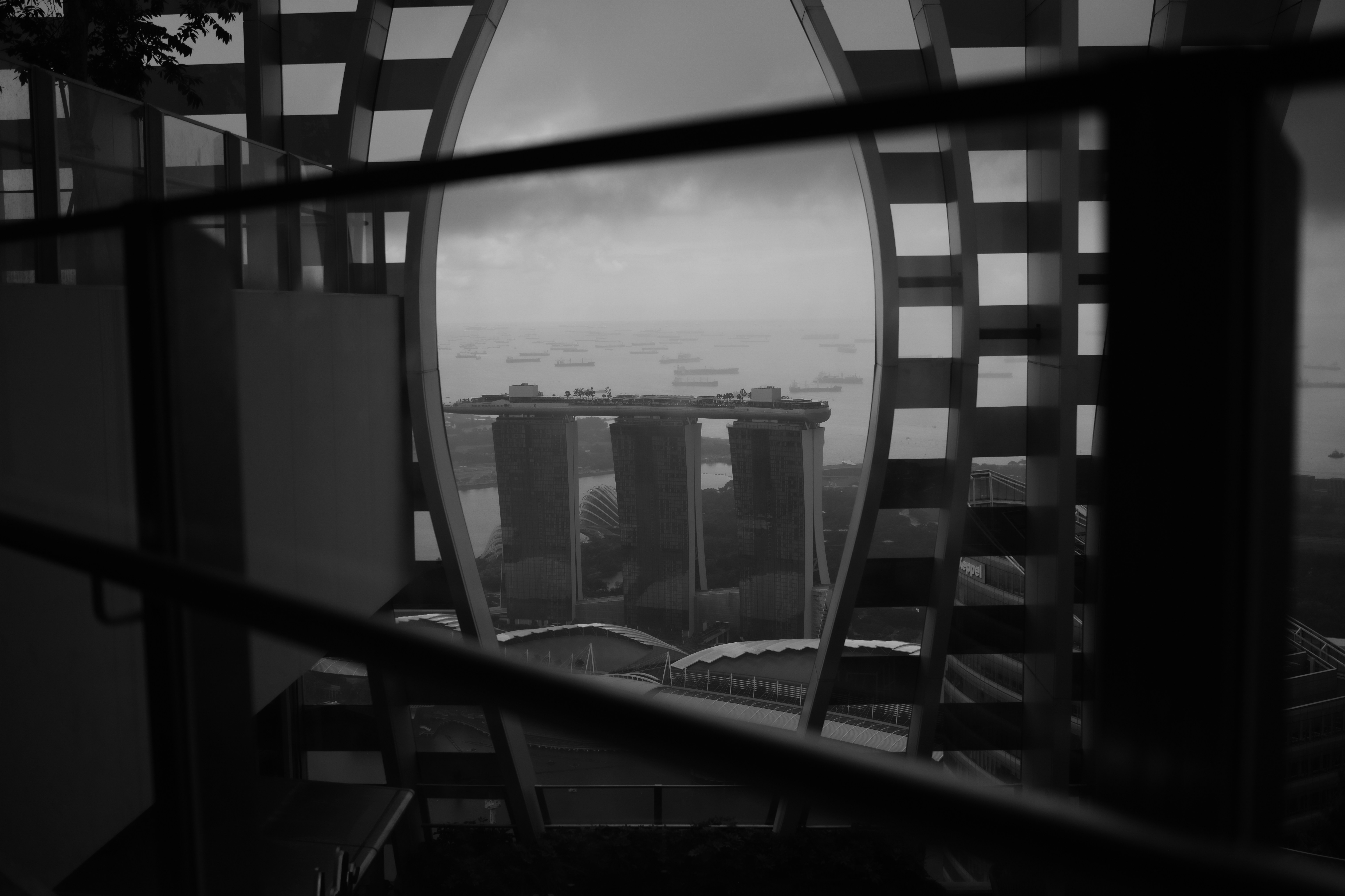 Monochrome view of city skyscrapers seen through a circular, lattice-like structure.