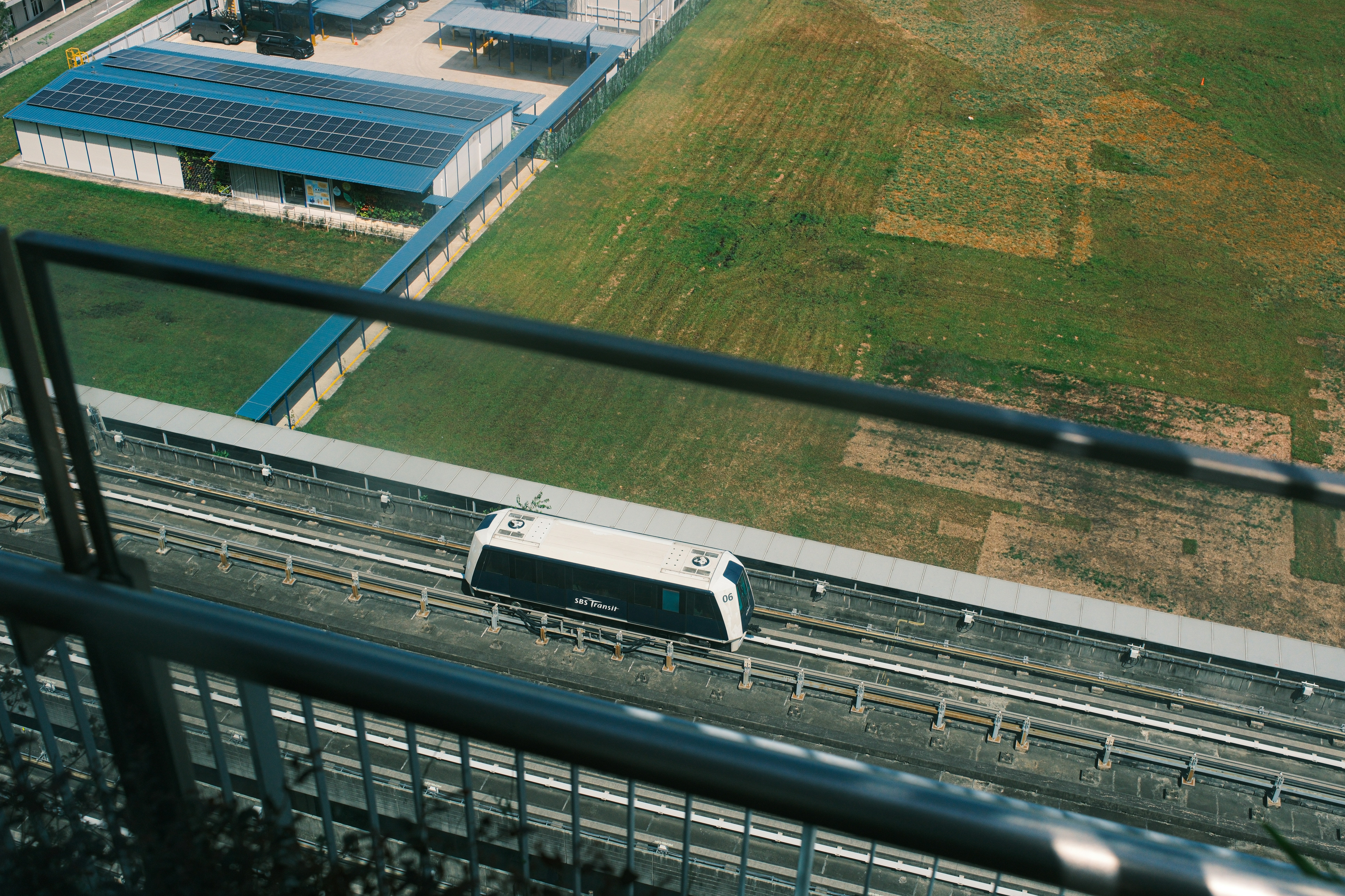 Aerial view of a monorail gliding along tracks beside a patchwork of fields and industrial buildings.