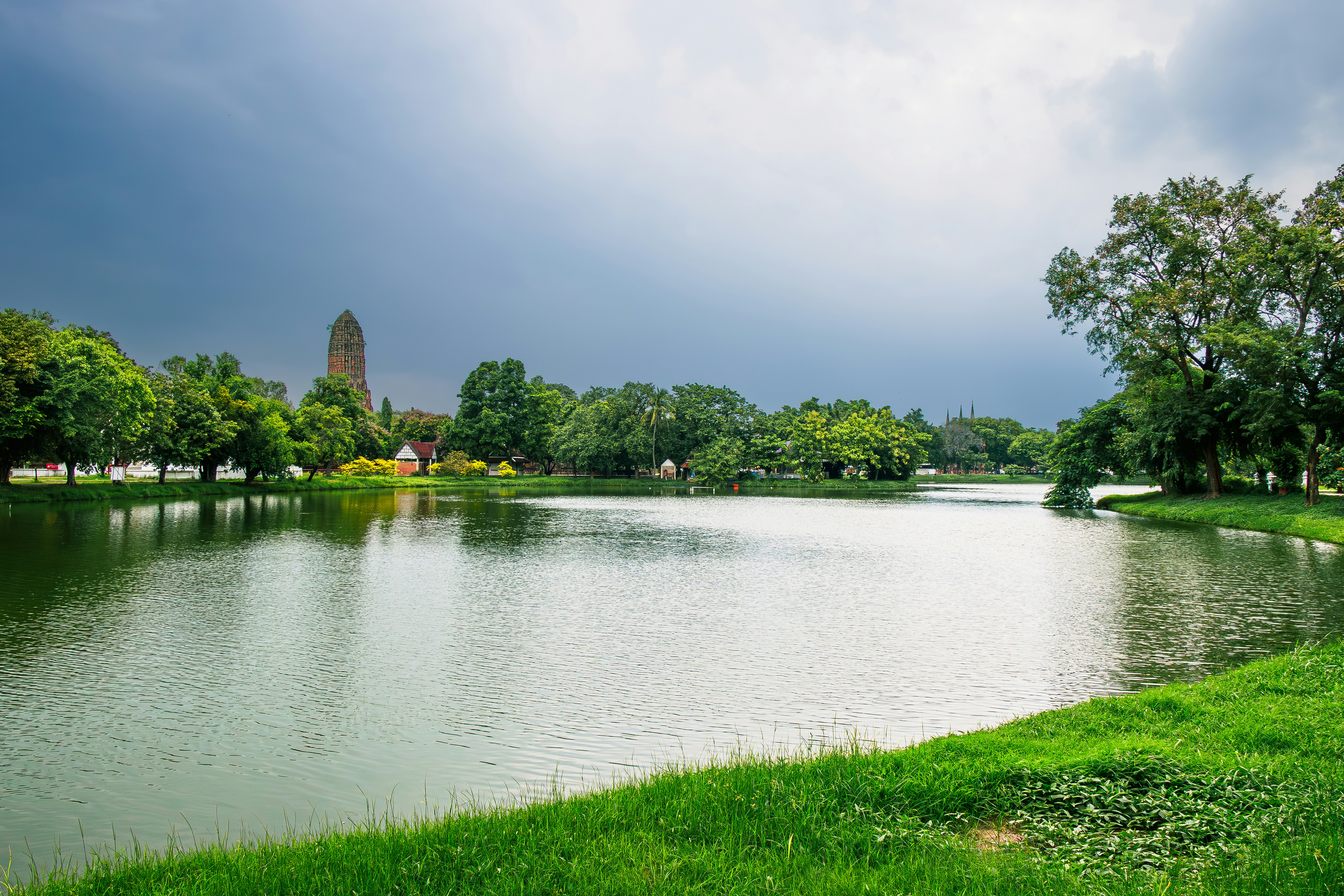 Lush green parkland surrounding a calm lake under a dramatic cloudy sky.