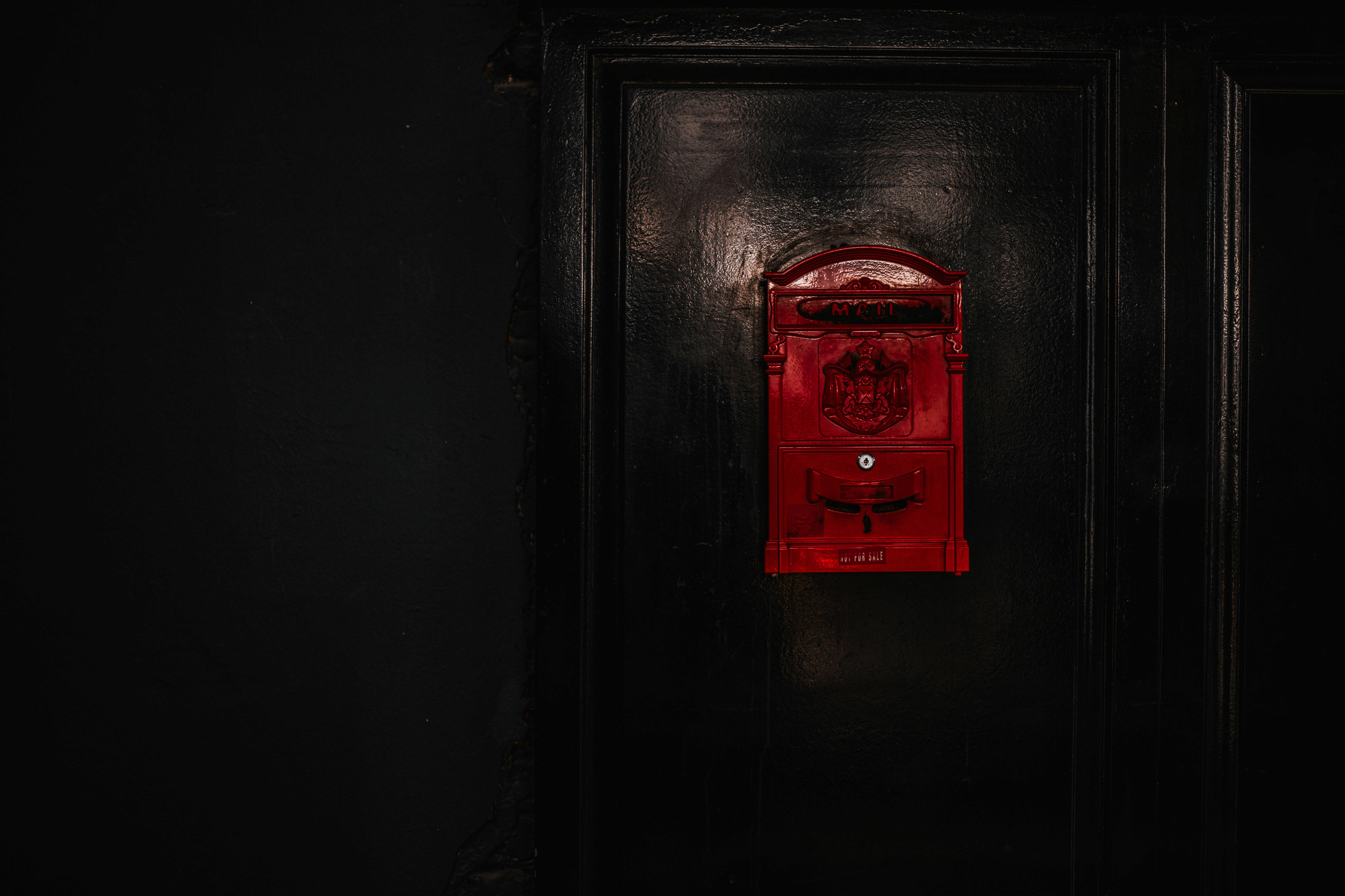Dim hallway scene featuring a single red fire alarm box mounted on a glossy black wall. The red unit stands out starkly against the subdued surroundings.