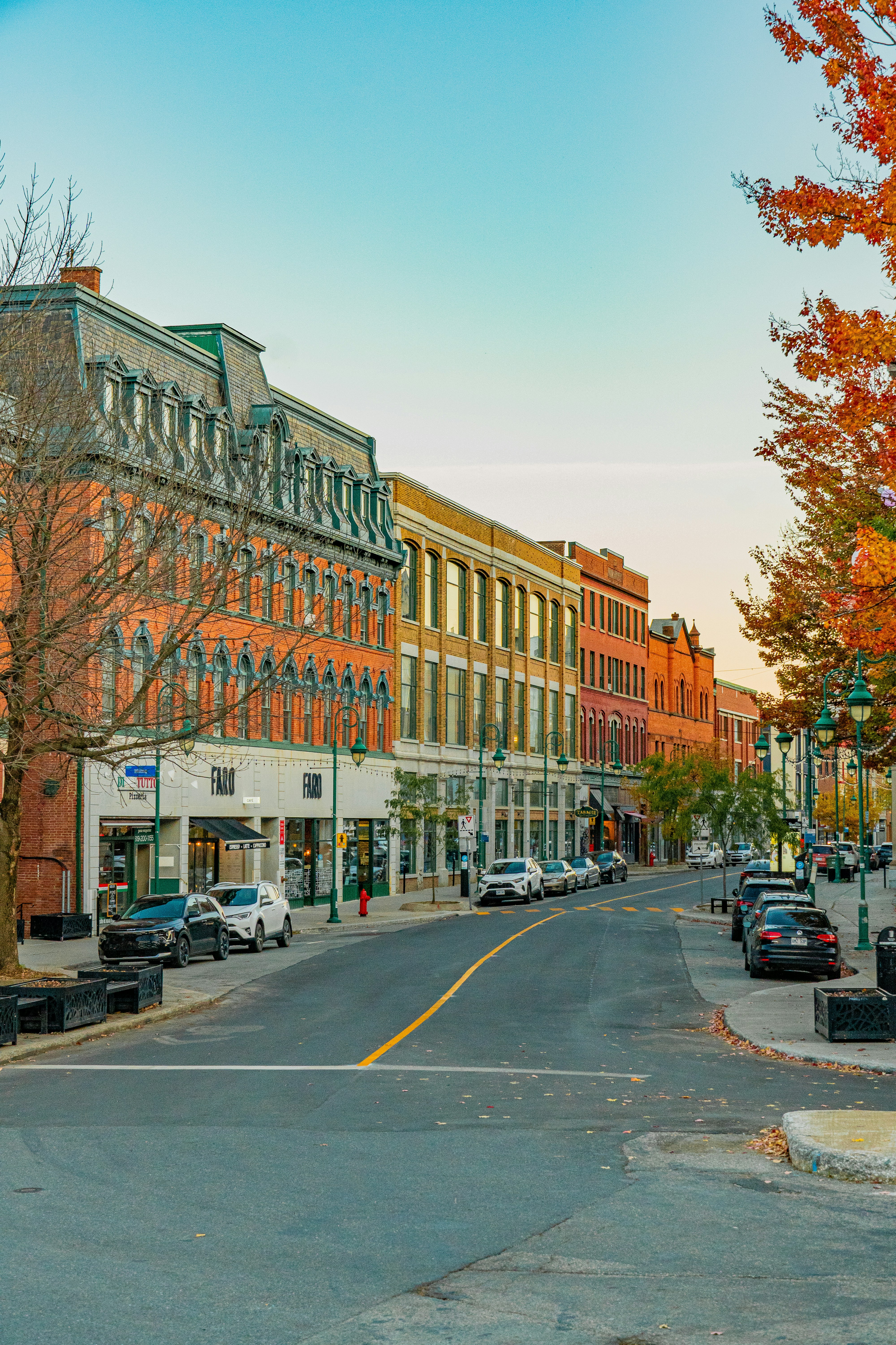 Colorful historic buildings line a quiet street under a clear blue sky with autumn trees in full foliage.