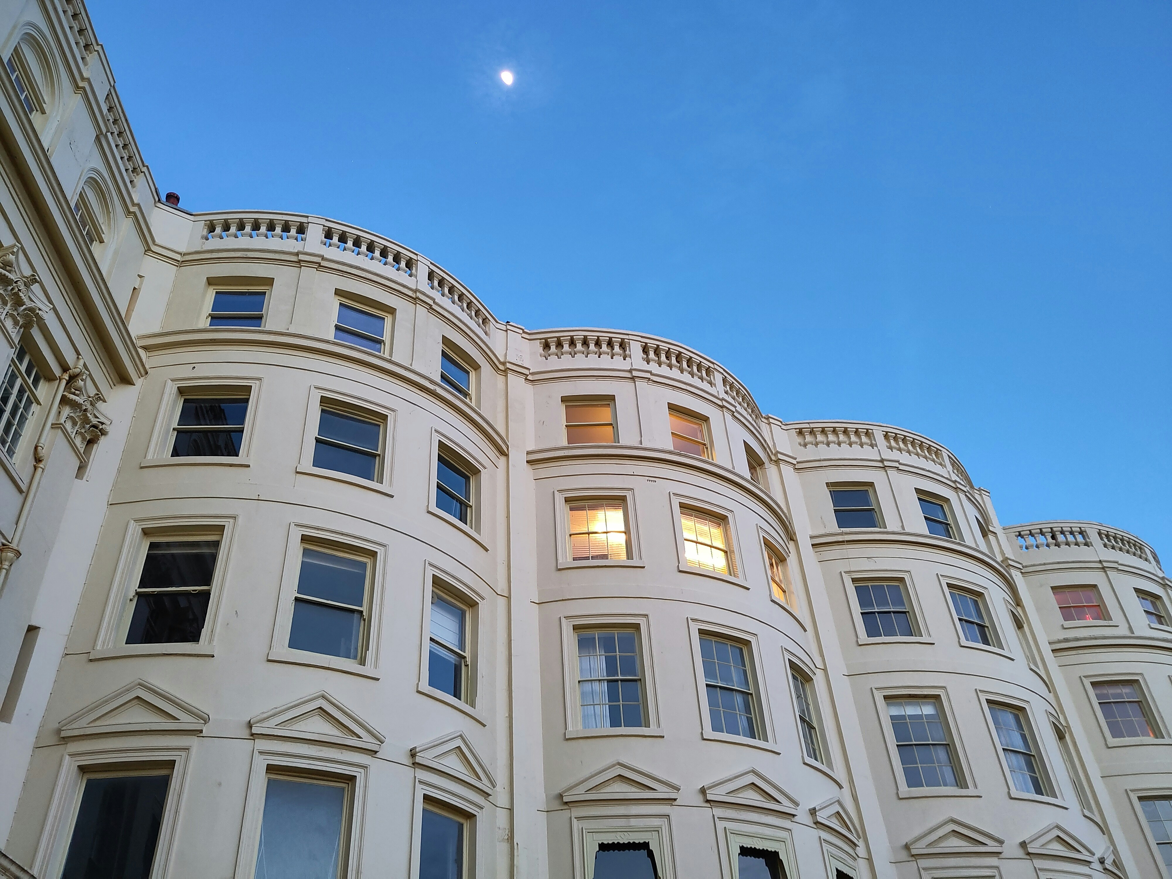 Curved facade of a historic building under a twilight sky with a visible crescent moon.