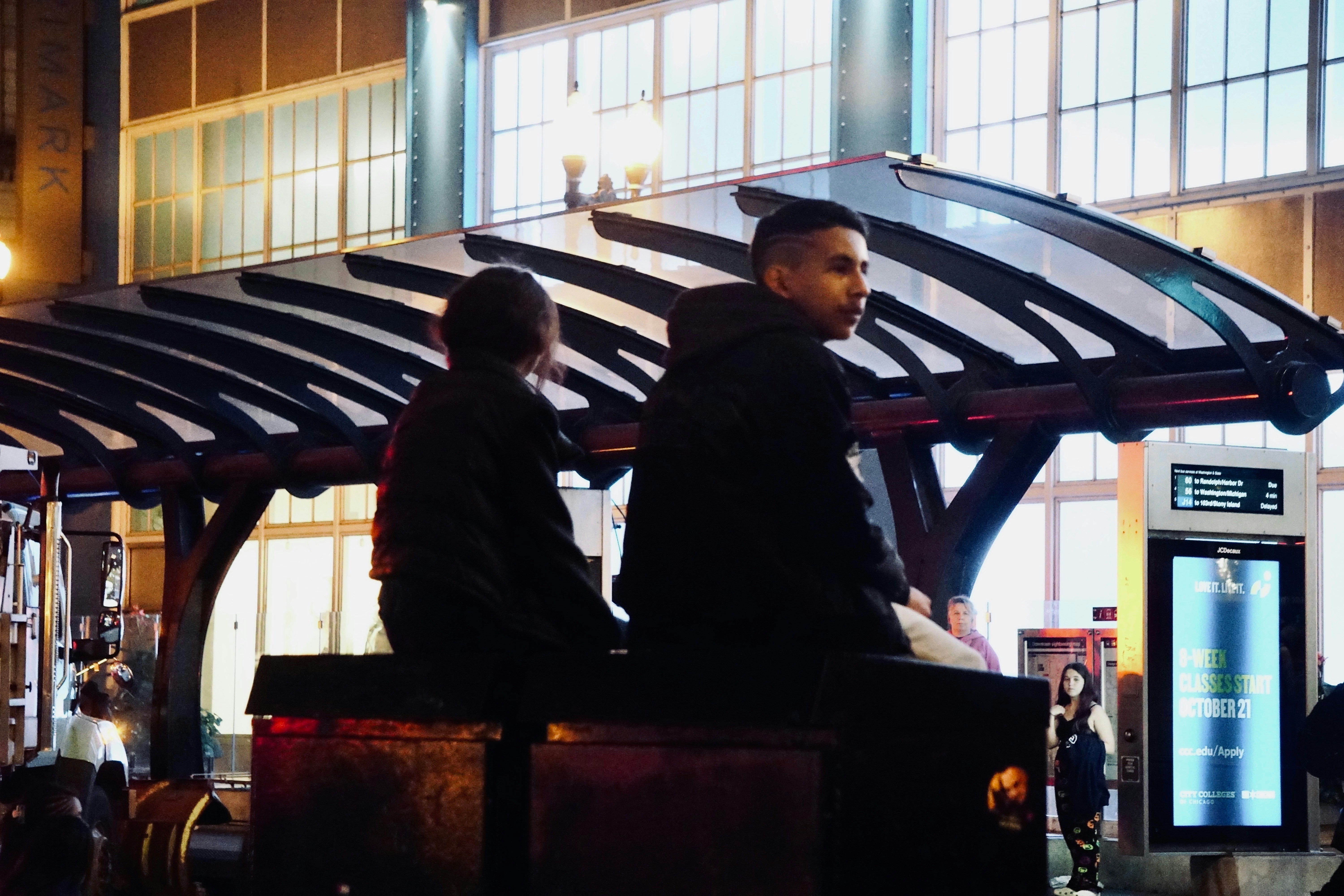 Two individuals seated on a carriage under an architectural canopy with city lights illuminating the scene.