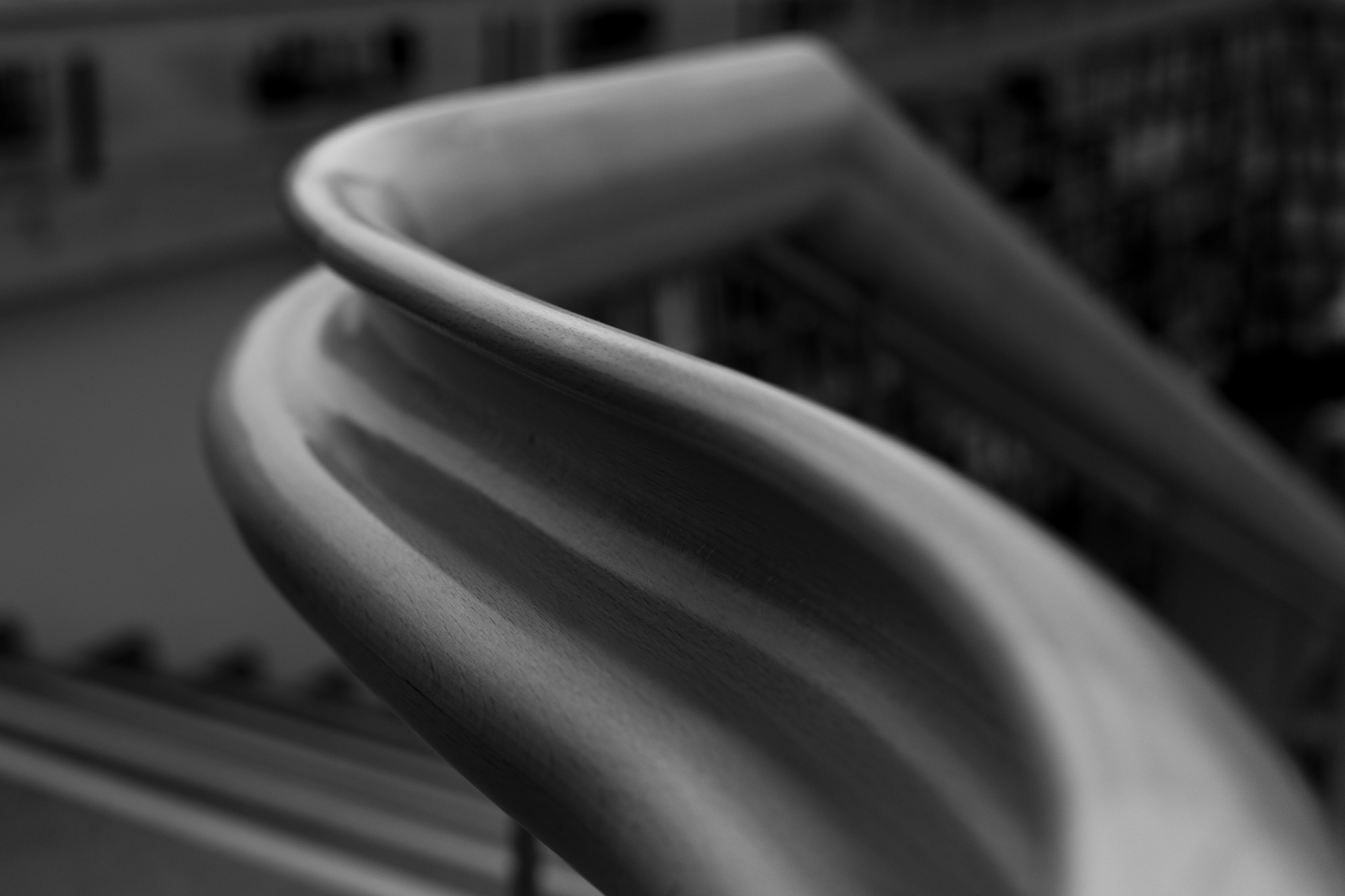Curved wooden handrail in focus against a blurred staircase backdrop.
