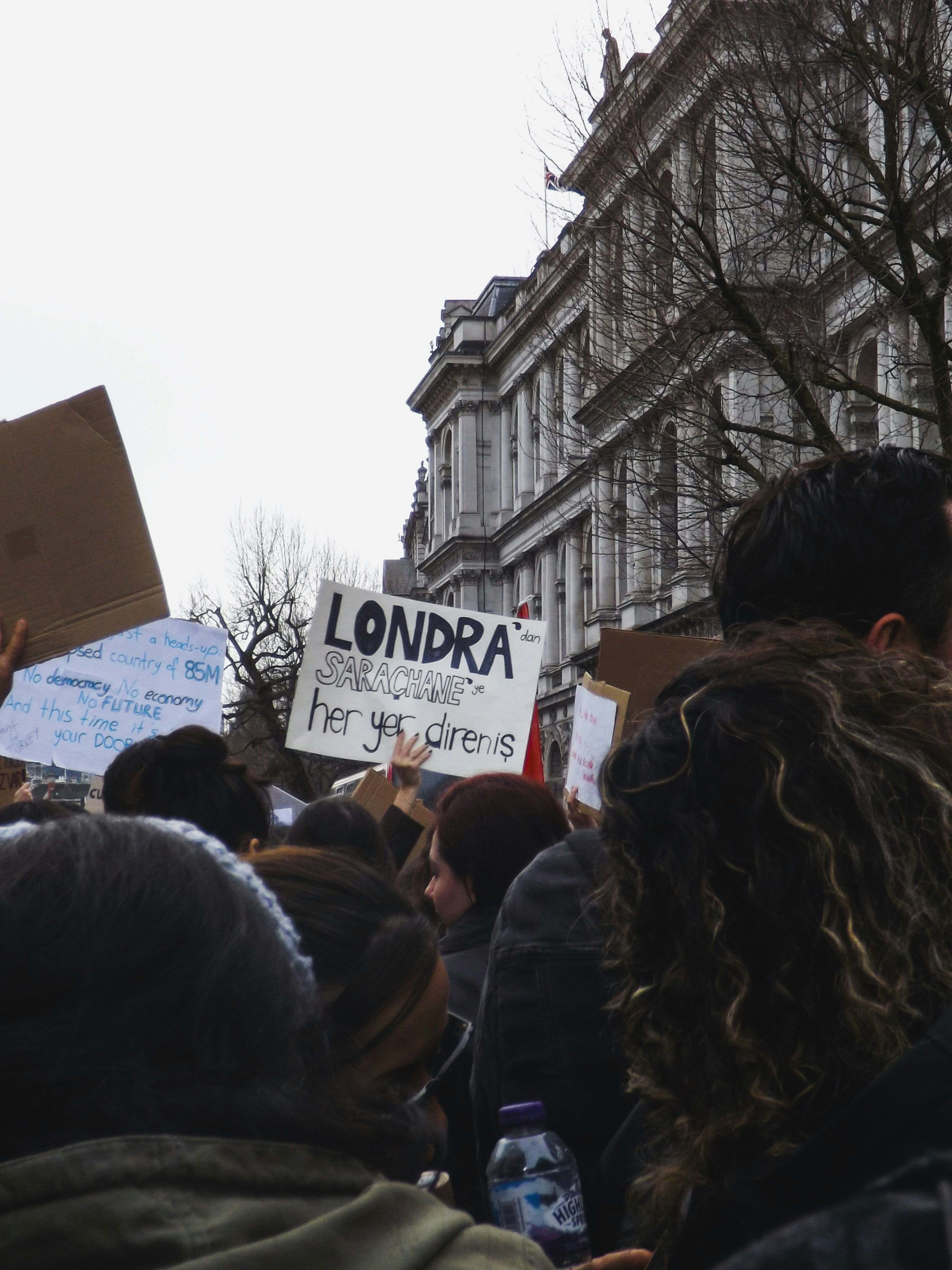 Crowd holding protest signs in a city street, with a focus on a prominent sign reading 'LONDRA'.