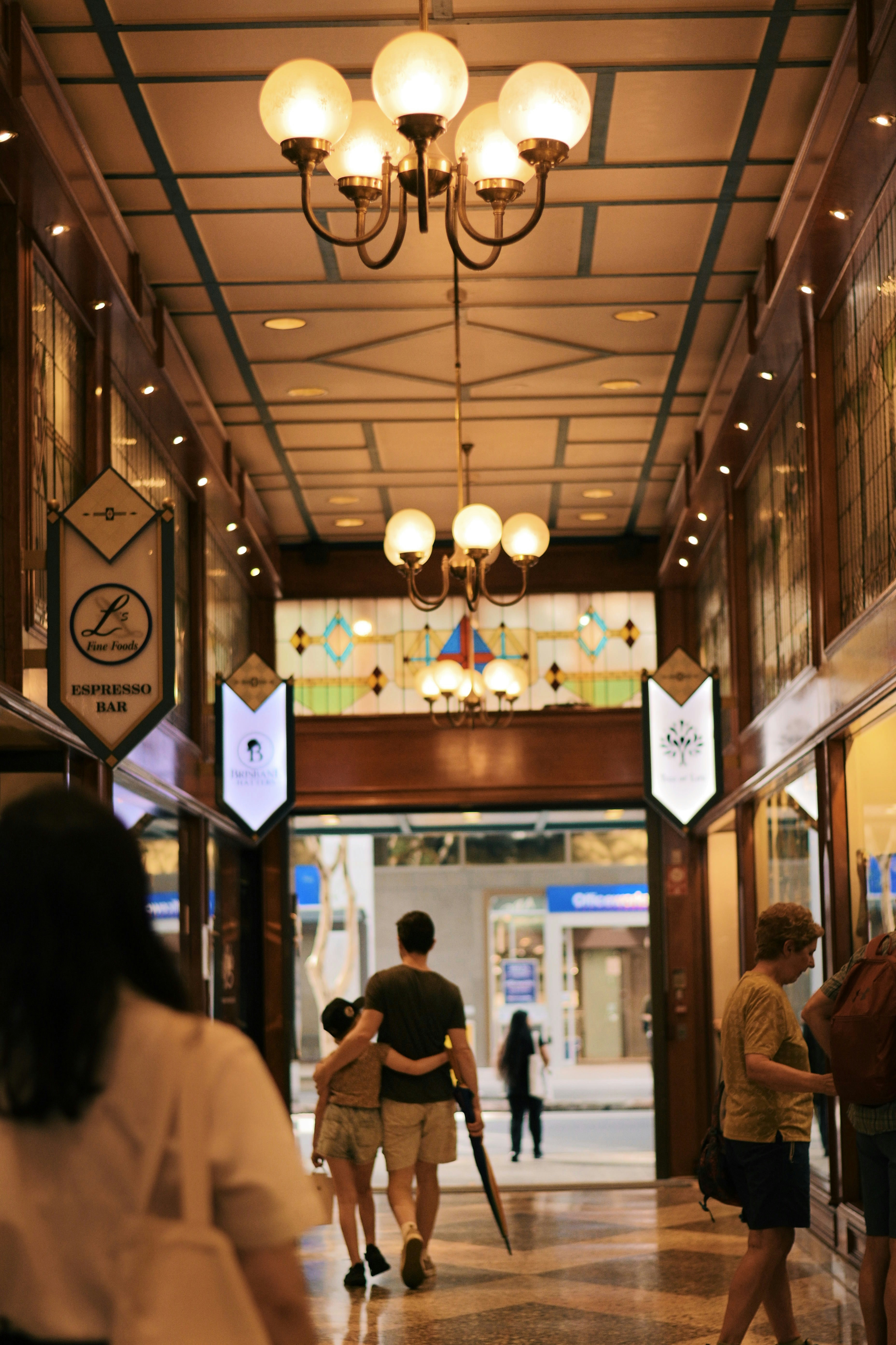 People walking through a vintage arcade with ornate lighting and stained glass accents.