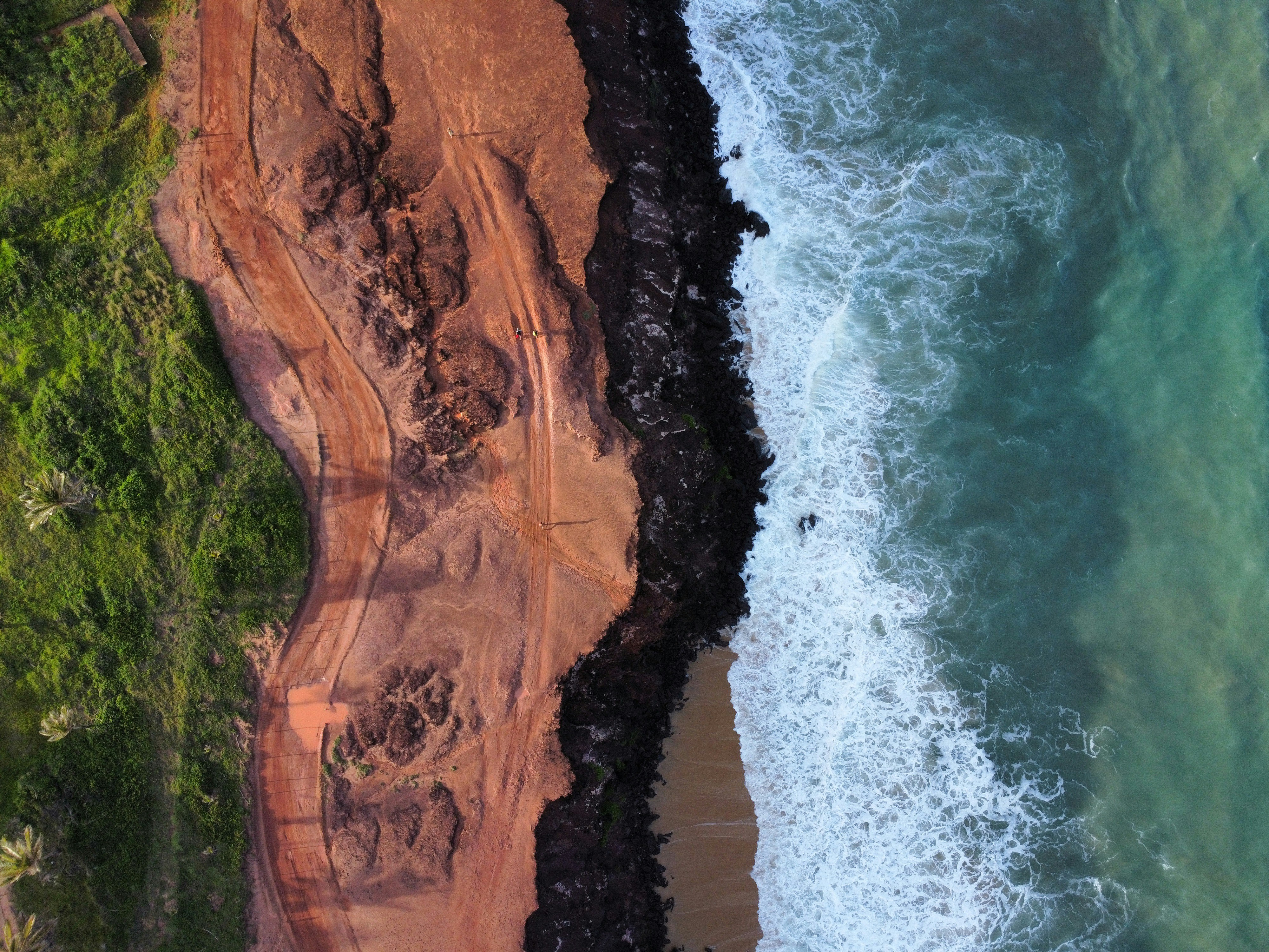 Aerial view of a vibrant coastline where lush greenery, rugged rocks, and turquoise waves converge.