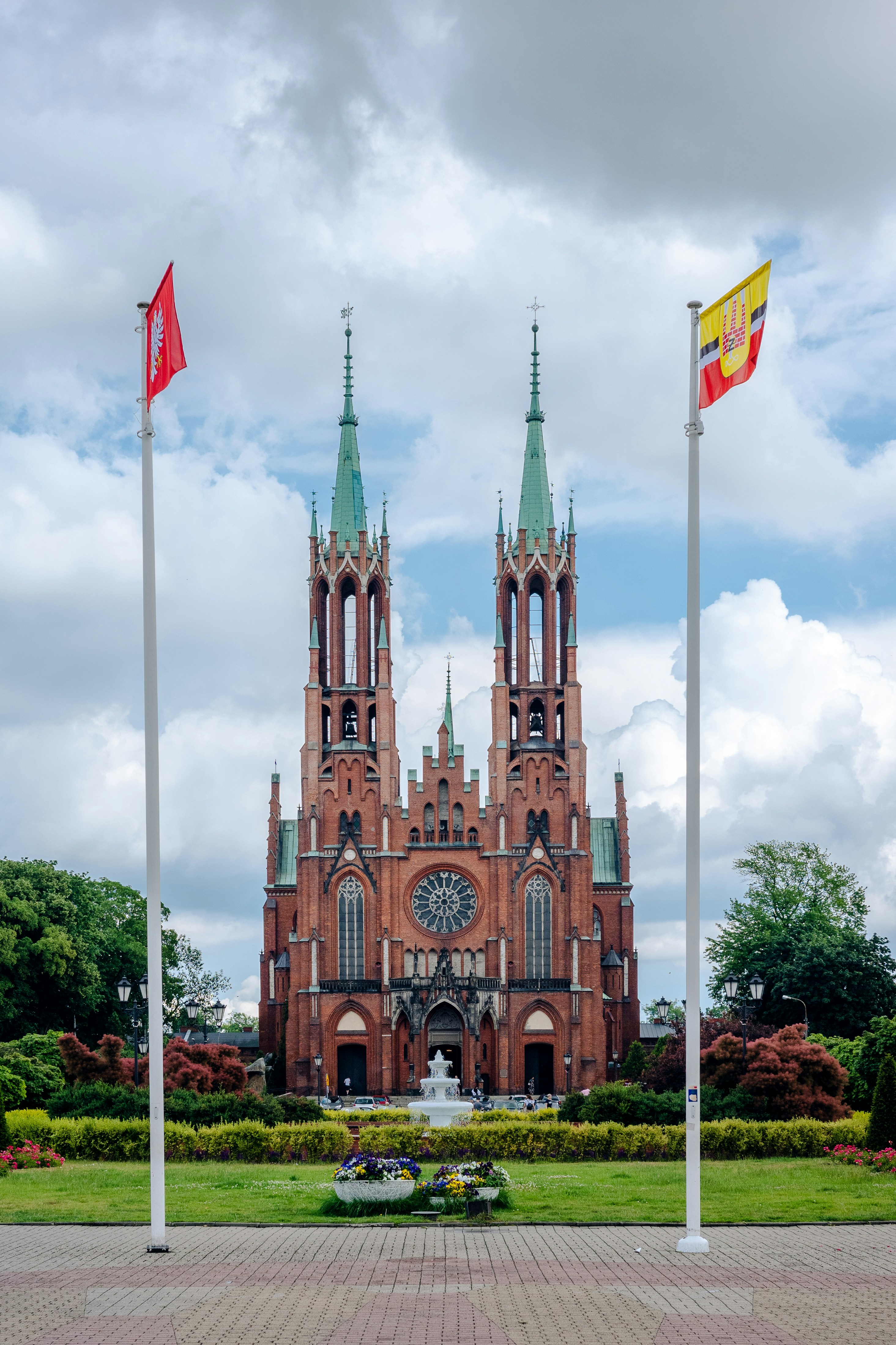 Flanked Cathedral: Red-Brick Twin Spires Rising Over a Sunlit Plaza