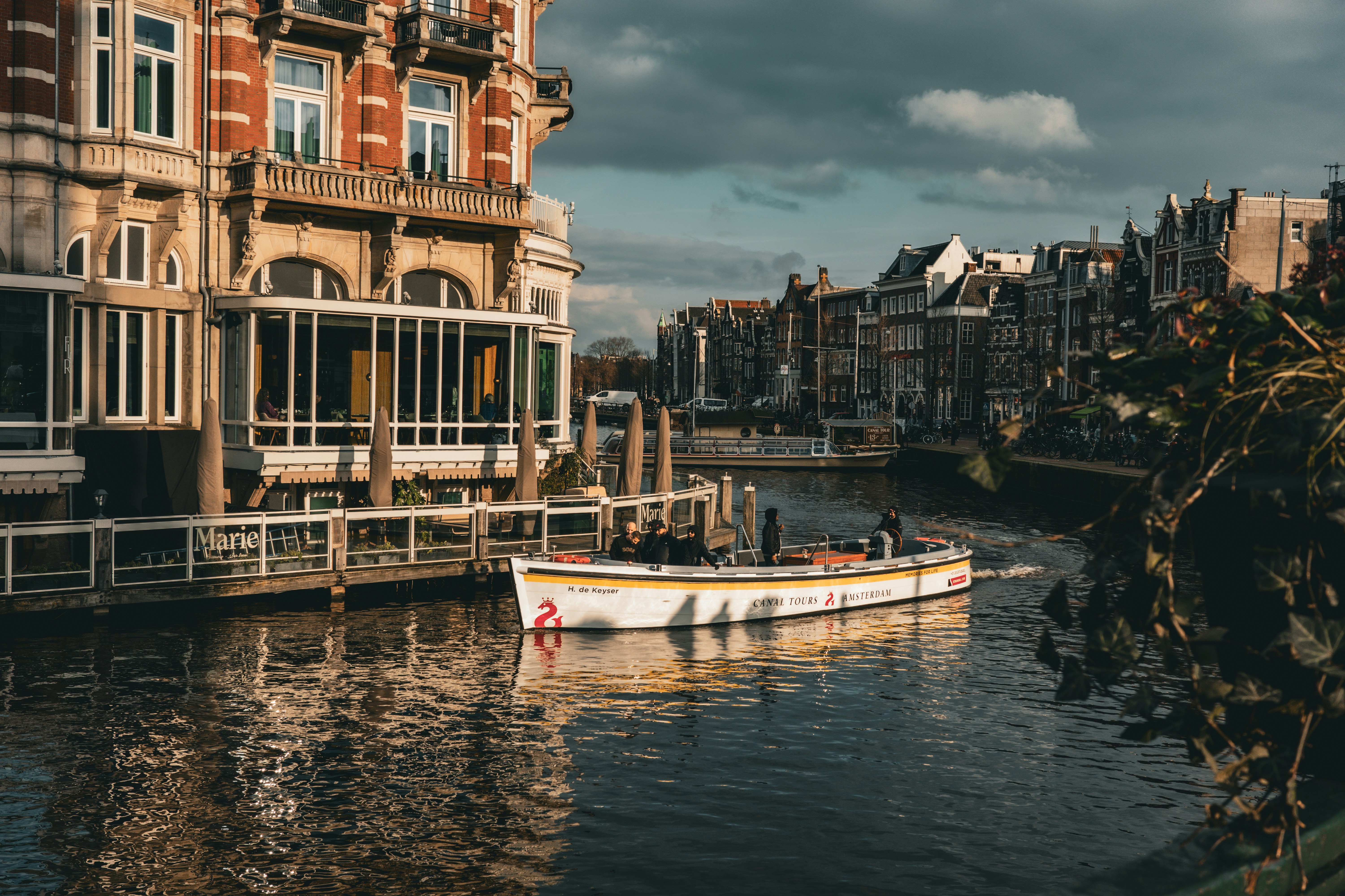 Small boat gliding through a sunlit canal beside historic buildings under a cloudy sky.