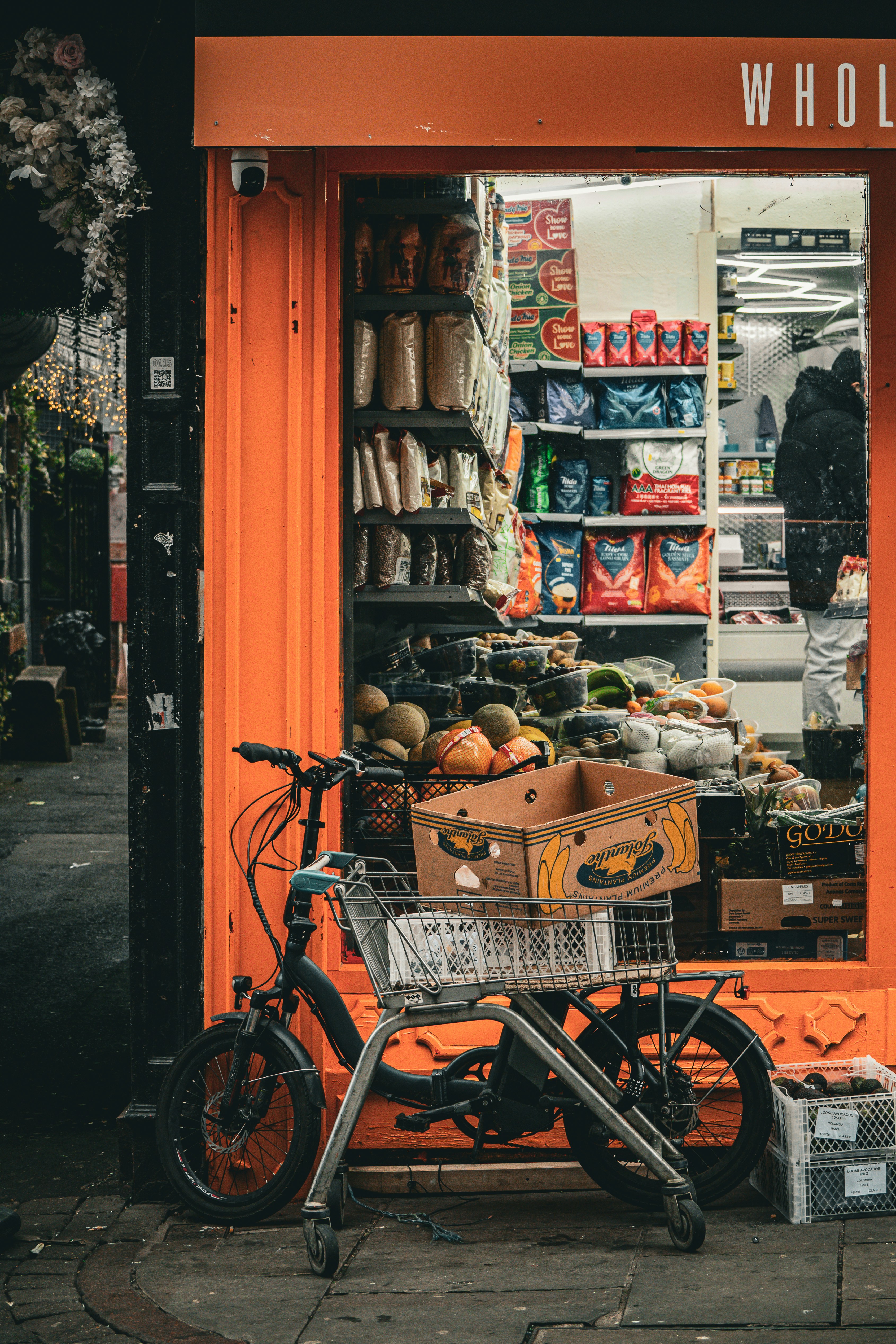 Cargo bike under a vivid orange storefront, brimming with produce