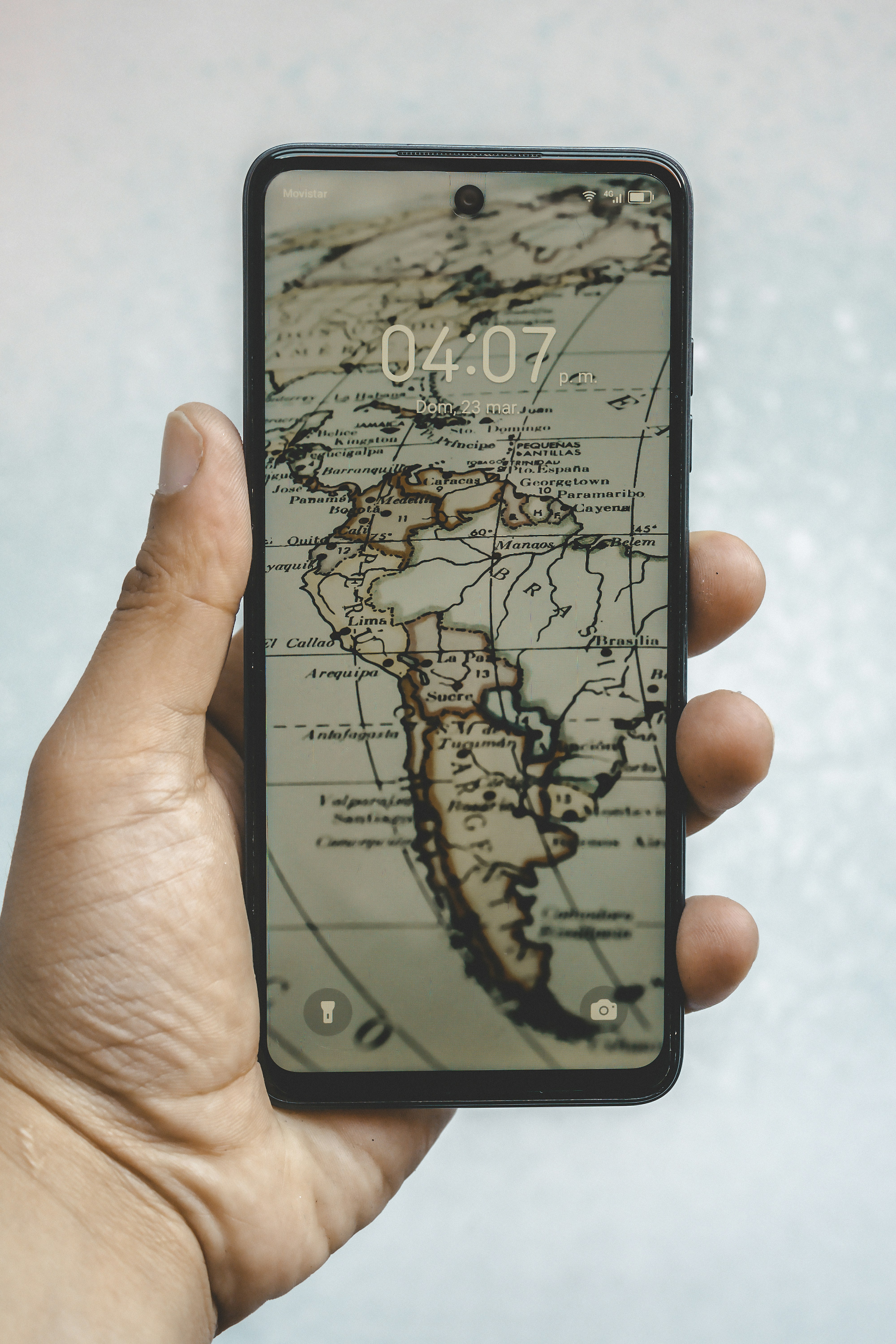Smartphone displaying a vintage map of South America with a time and date overlay. The hand holding the device adds a personal touch to the historical context.