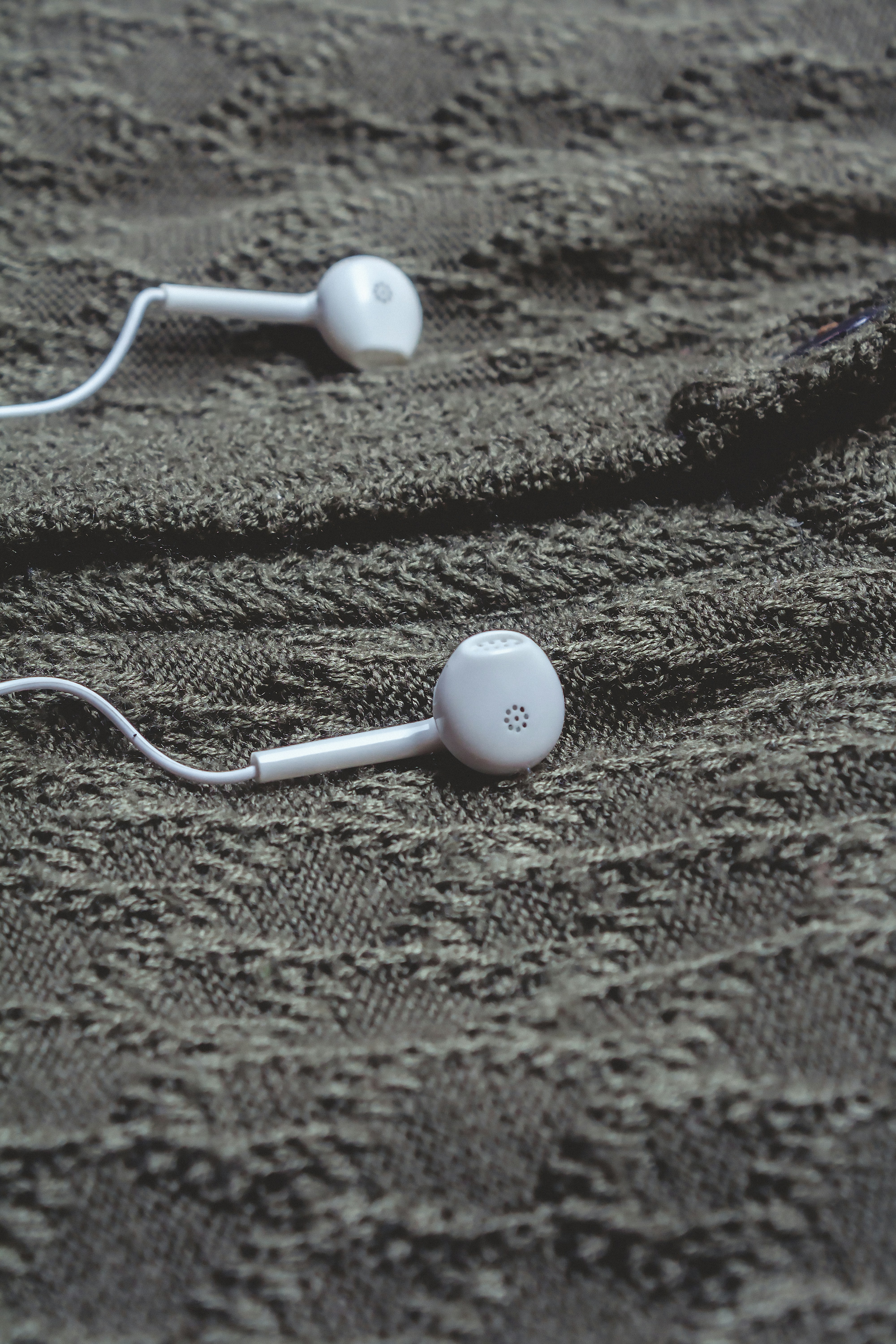 Pair of white wired earbuds rests on a textured brown fabric surface. The close-up highlights the contrast between smooth plastic and the fabric's intricate weave.
