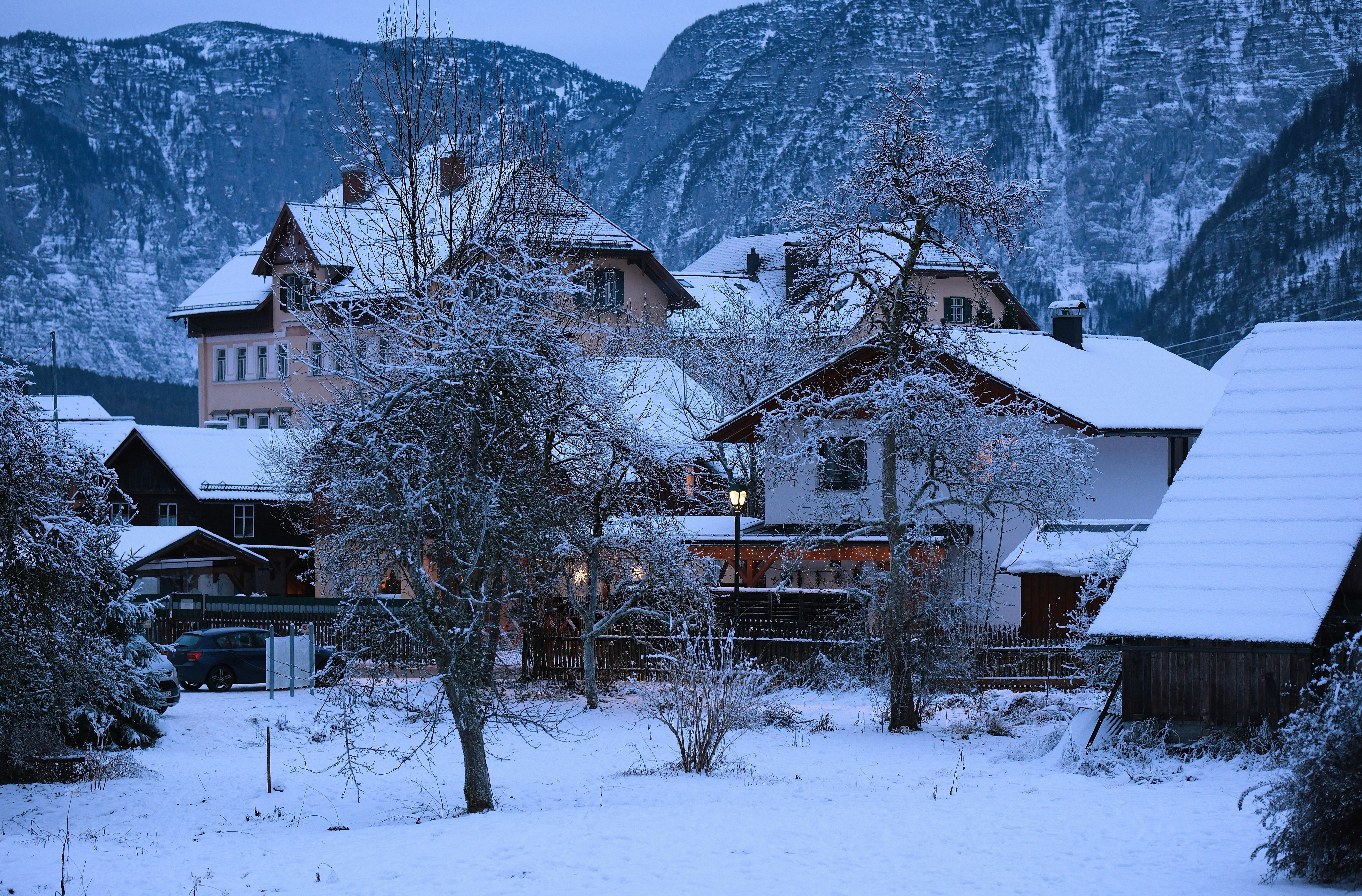 Snow-covered alpine village with rustic wooden houses and mountainous backdrop at dusk.