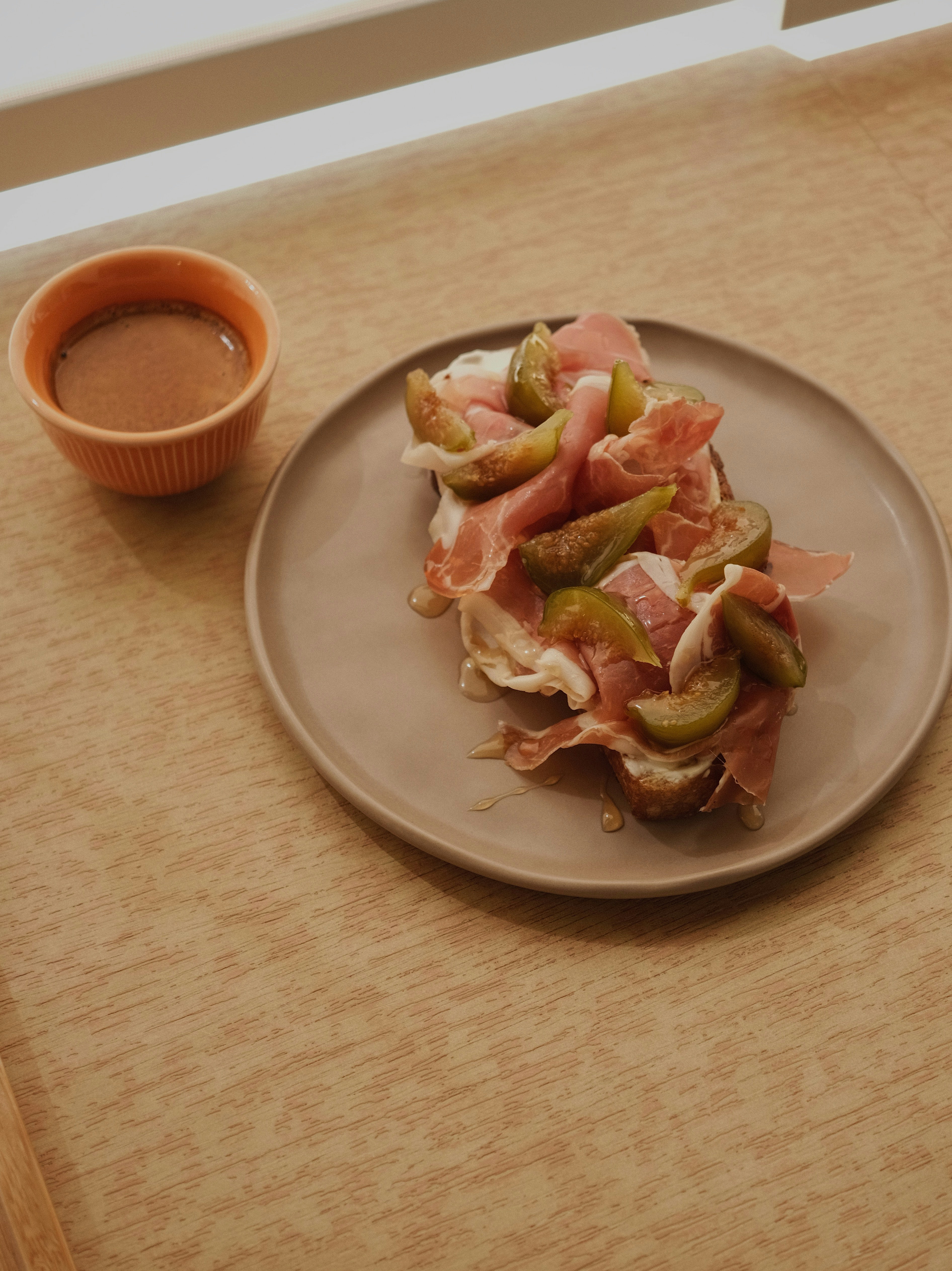 Artfully arranged dish featuring crusty bread topped with prosciutto, fresh figs, and a side of dipping sauce.