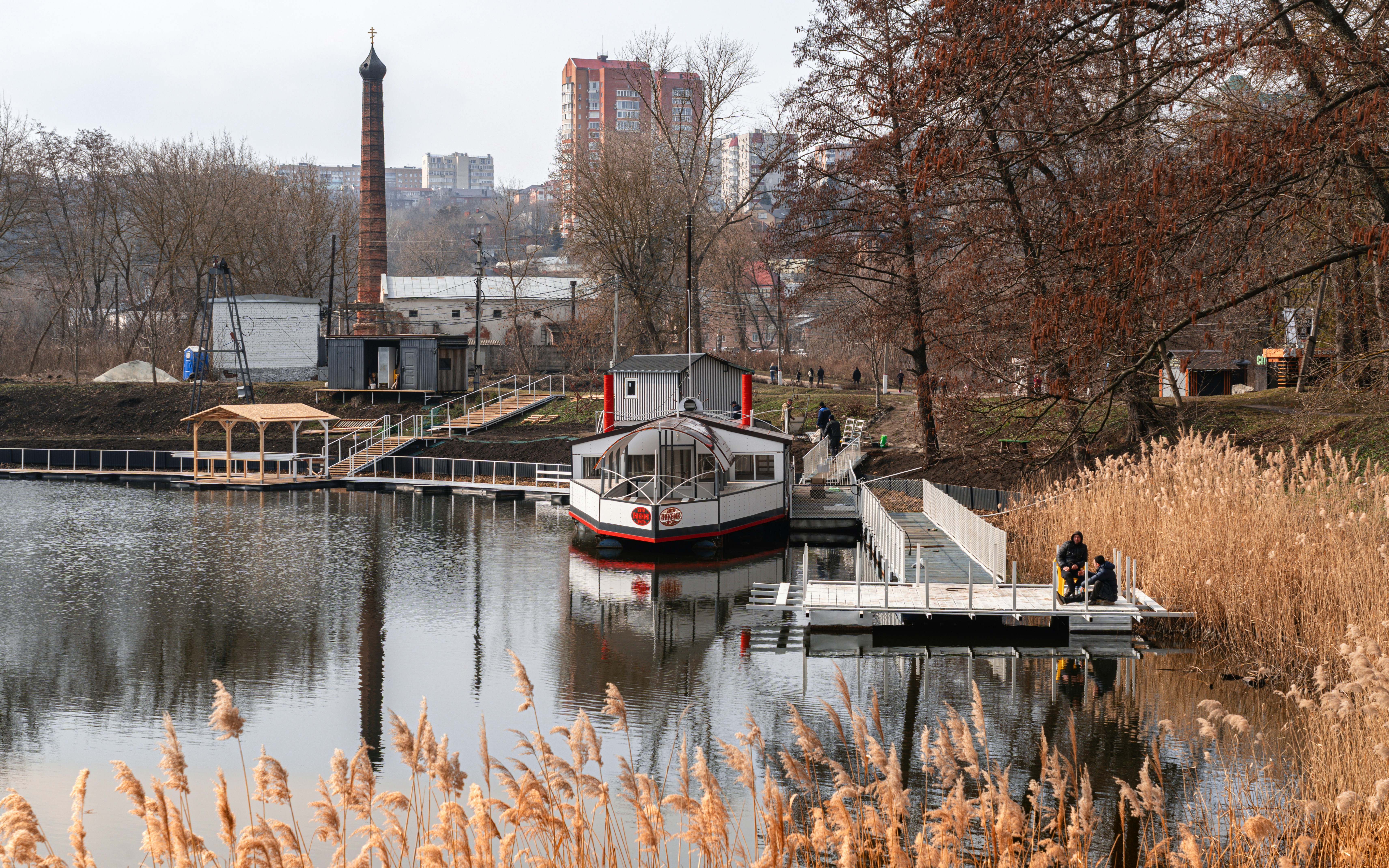 Quiet harbor scene with a docked boat and reeds along the water's edge on an overcast day.