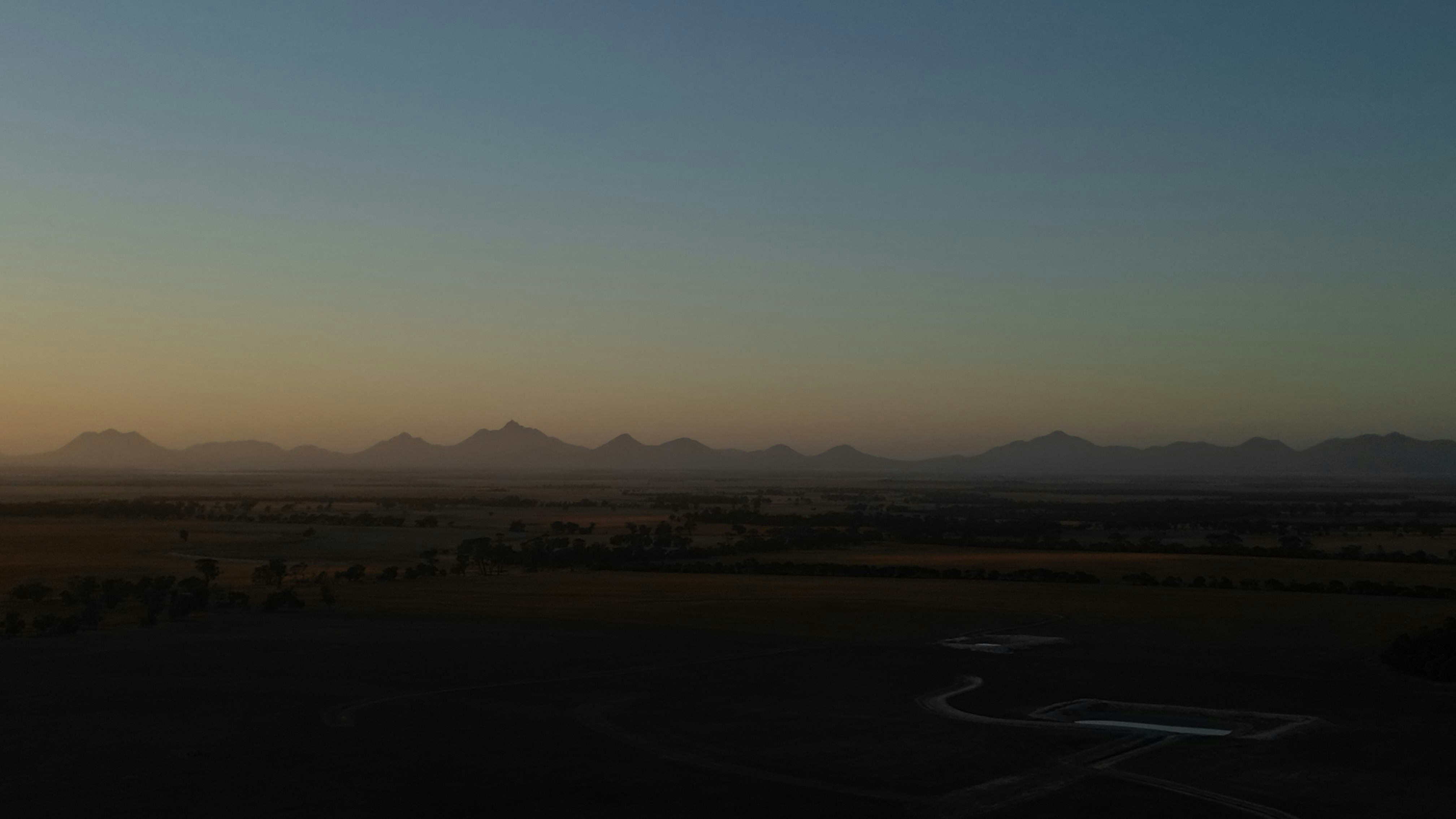 Dawn's Edge: Distant Peaks Silhouetted Across a Vast Desert Plain