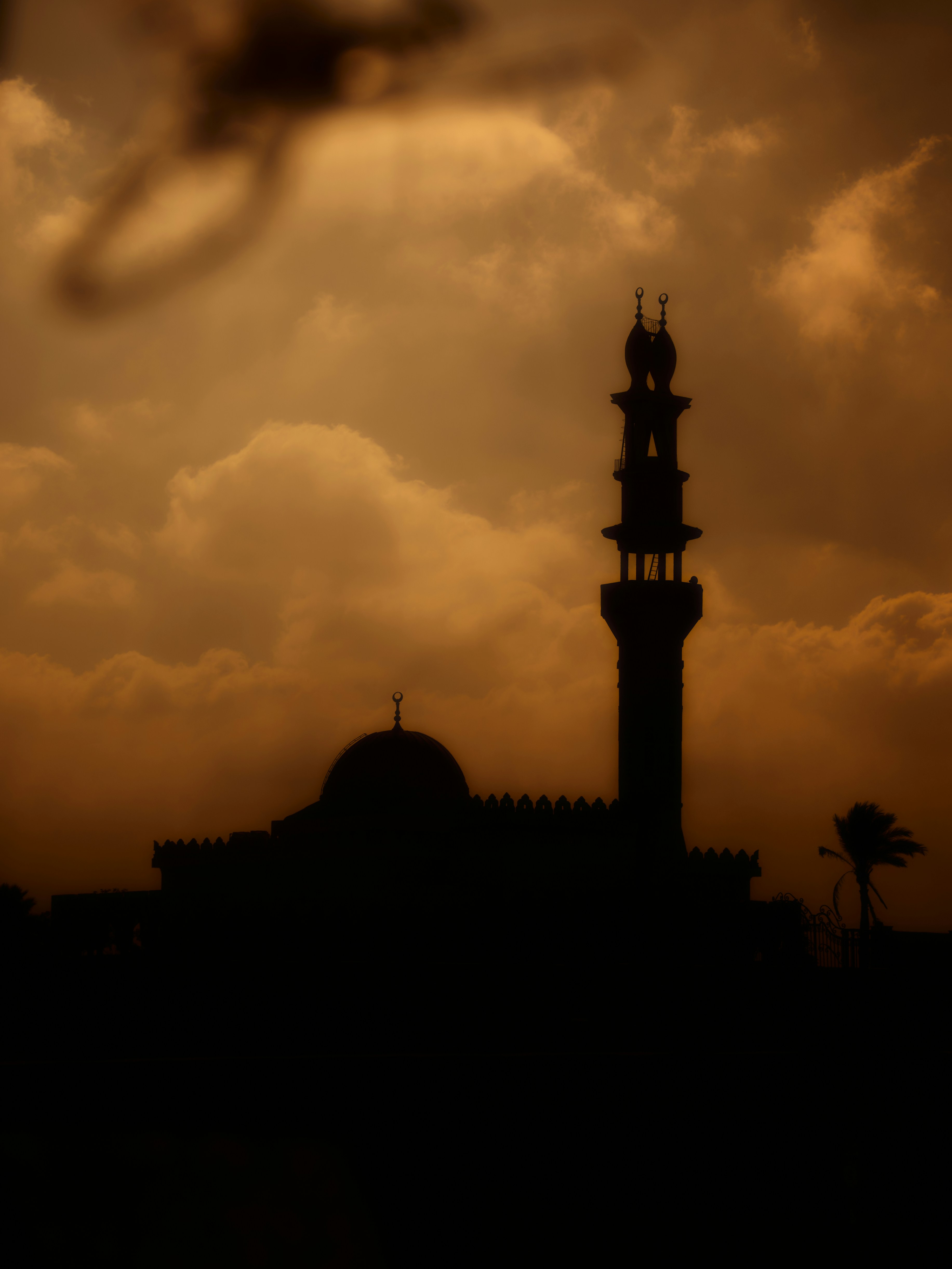 Silhouette of a mosque with a prominent minaret against a dramatic sunset sky, evoking a sense of tranquility and reverence.