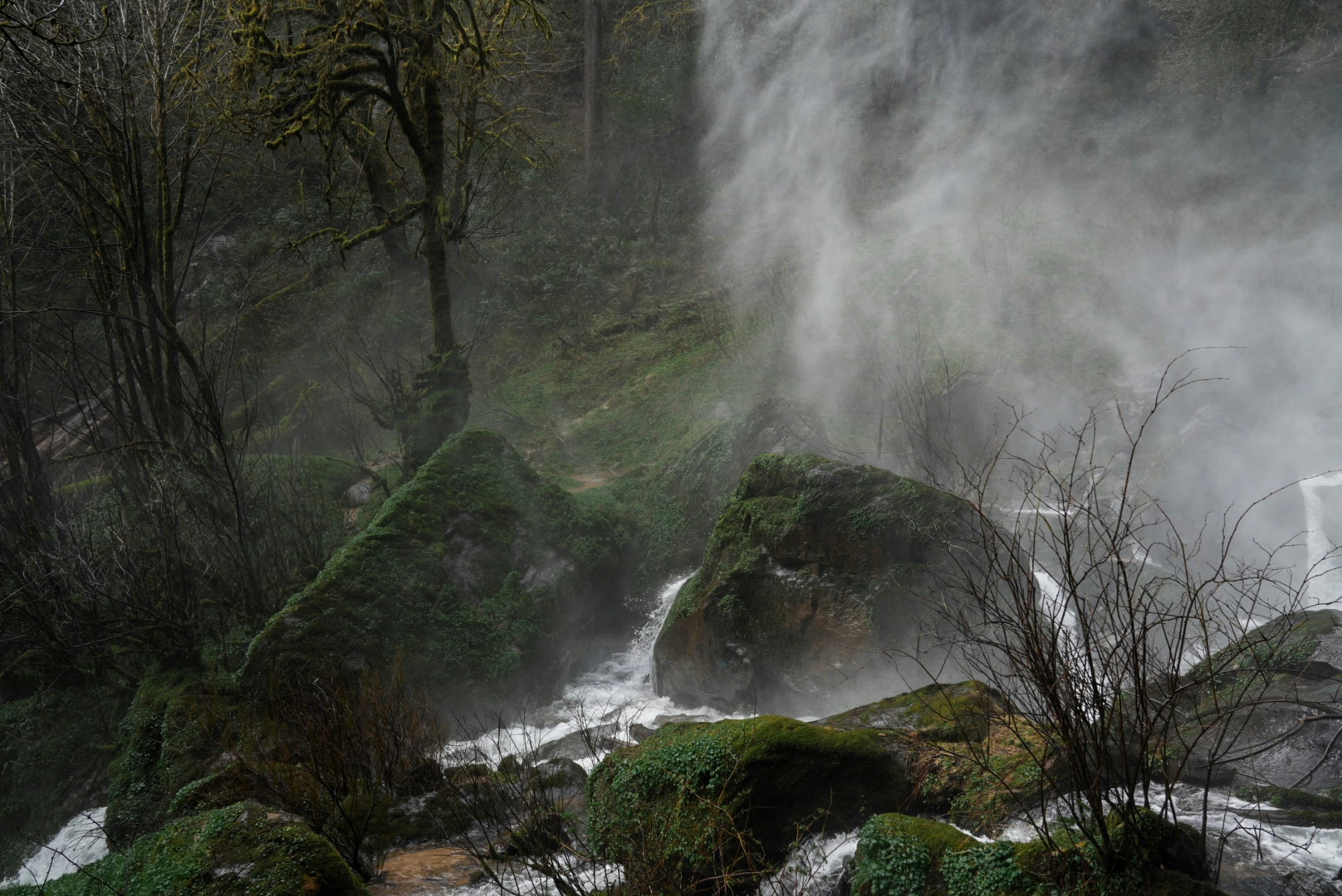 Misty waterfall cascading over moss-covered rocks in a lush, forested area.