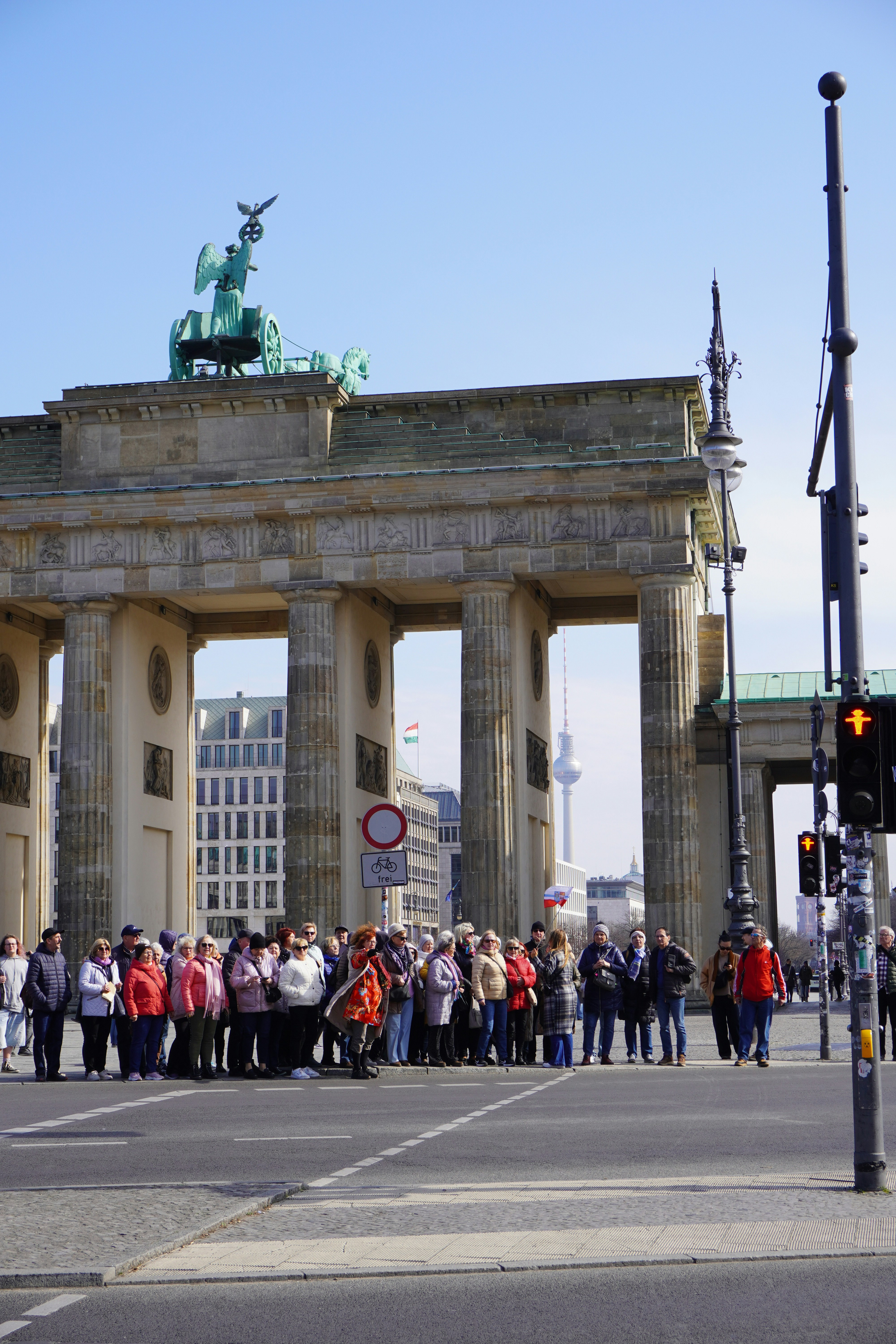Tourists gather in front of the historic Brandenburg Gate under a clear blue sky.