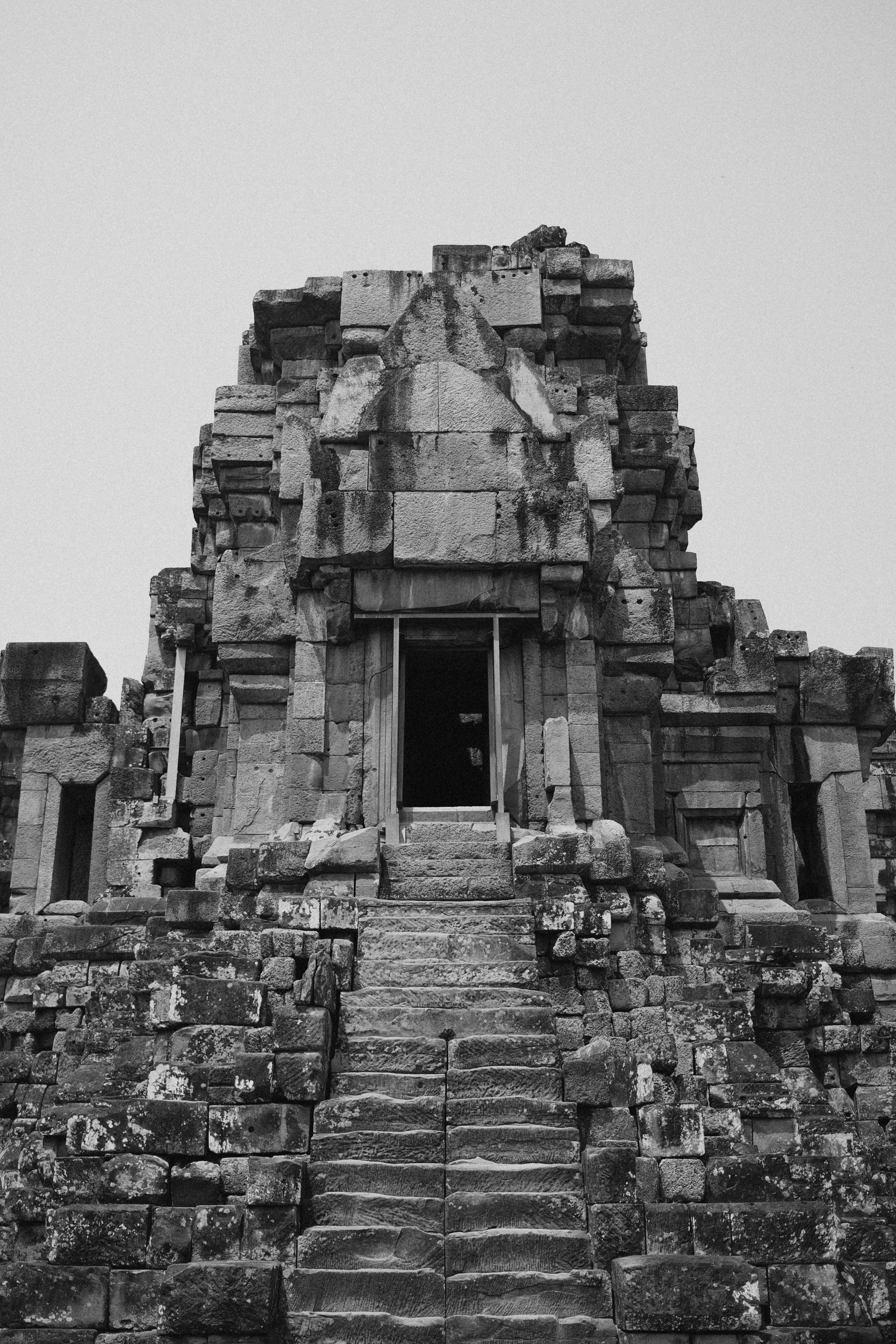 Majestic stone temple with weathered steps leading to a doorway, surrounded by ancient ruins. Black and white tones enhance the historical atmosphere.