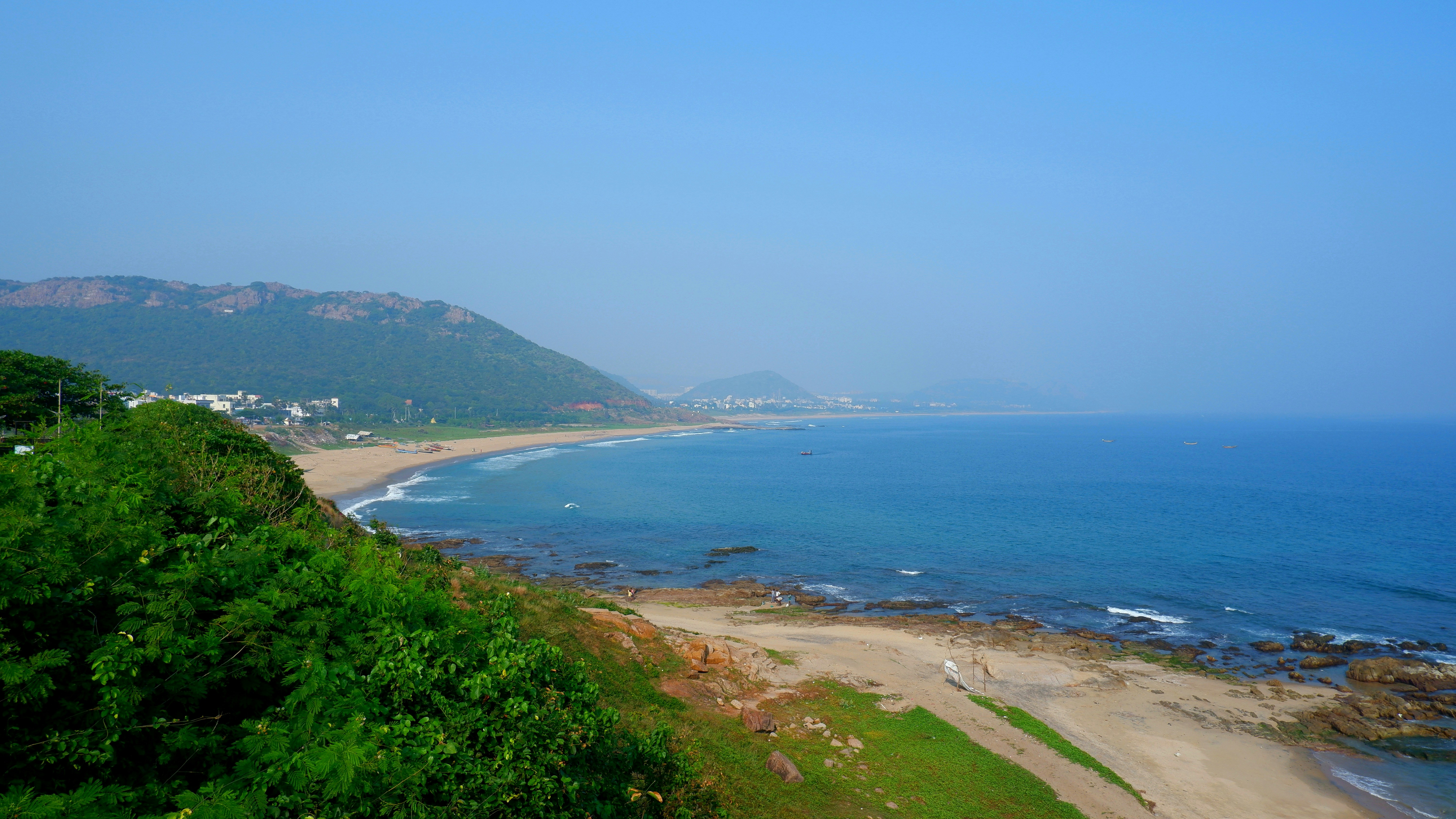 Coastline view with lush greenery, sandy shores, and the Bay of Bengal under a clear blue sky.