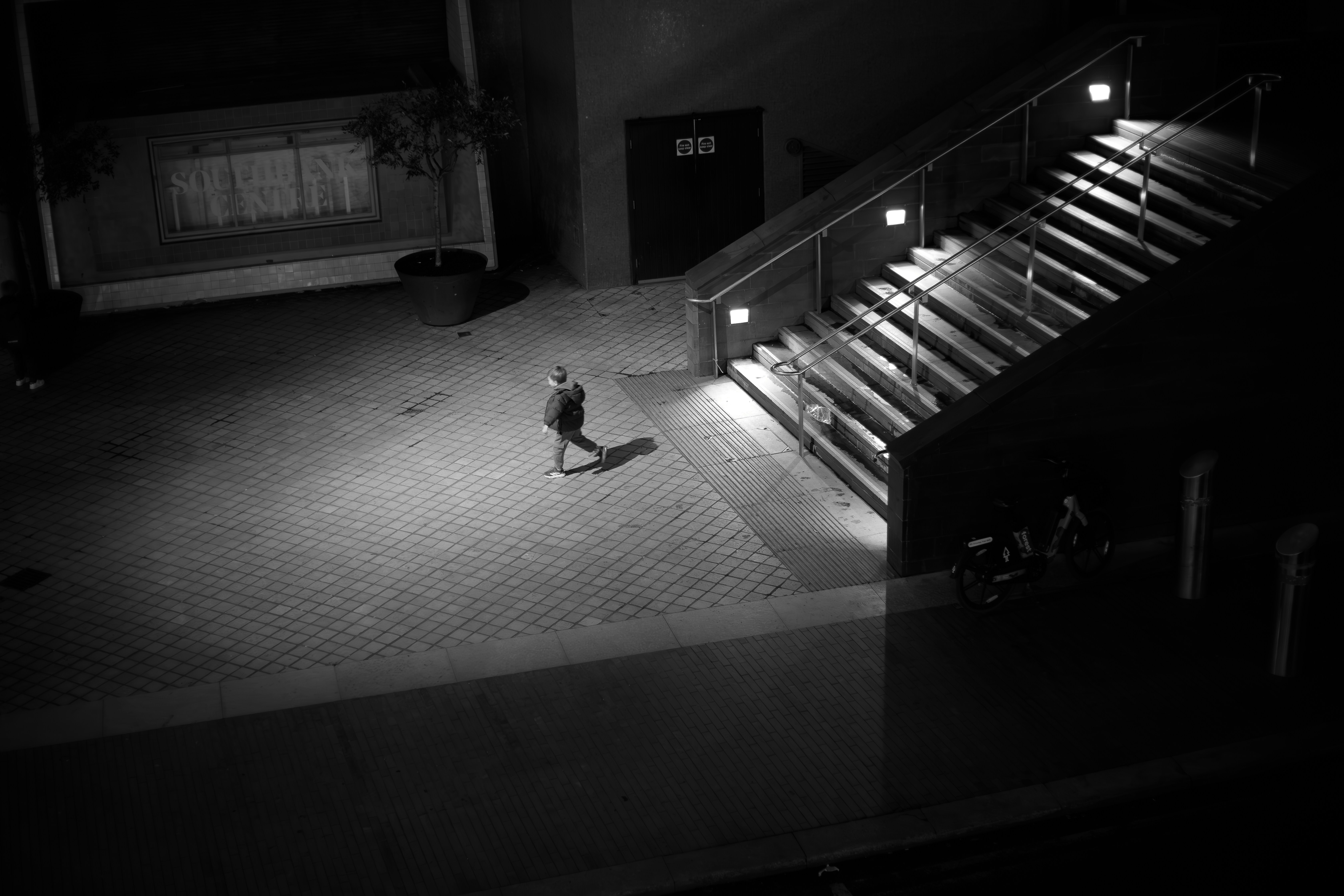 Person walking near illuminated stairs in a dimly lit urban setting.