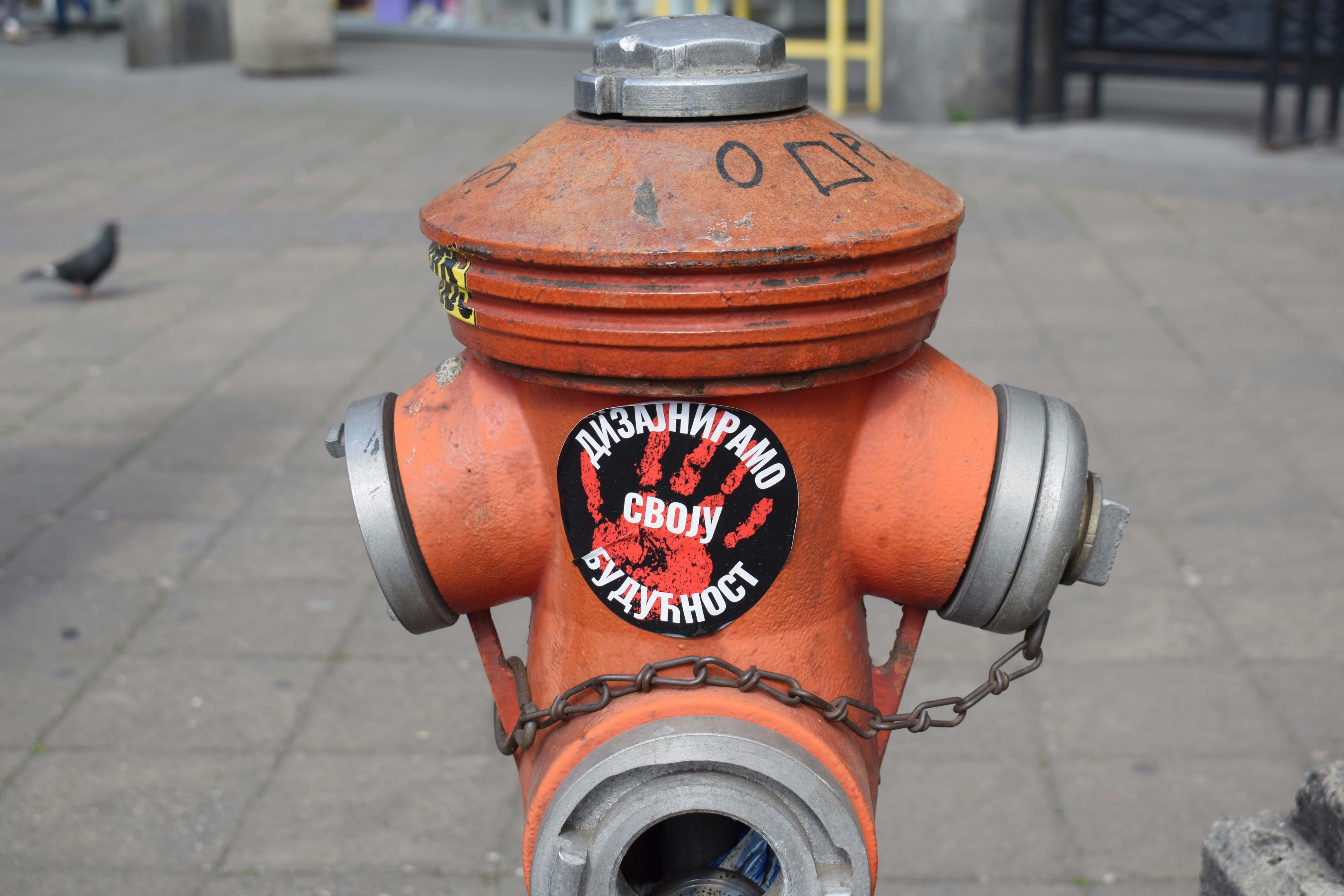 Stickered Orange Hydrant: Urban Sentinel in a Quiet Plaza