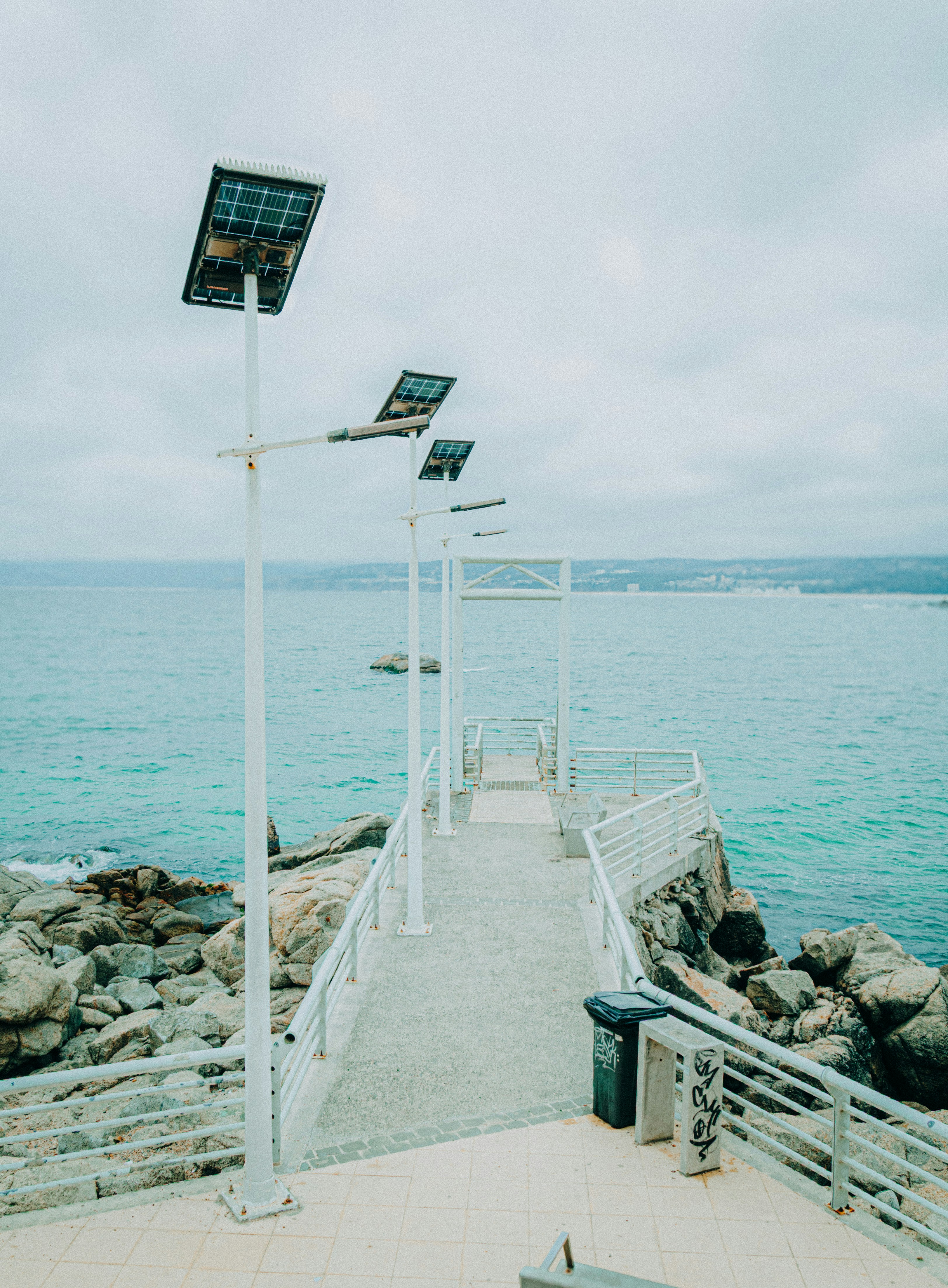 Pier with solar-powered lights extending over a calm, blue sea under a cloudy sky.