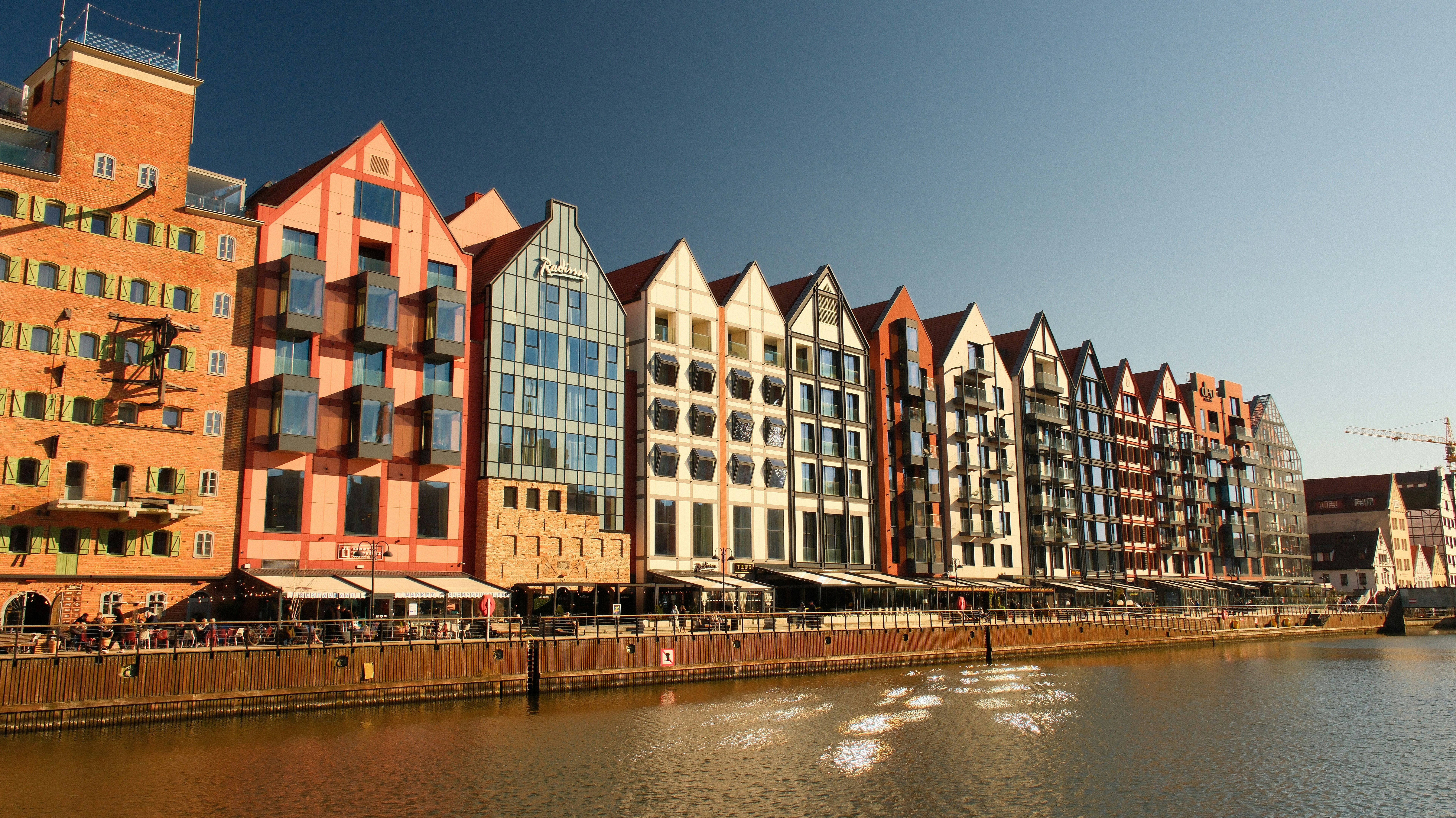 Sunlight dances on the Motława River beside colorful, gabled buildings blending modern and traditional architecture.