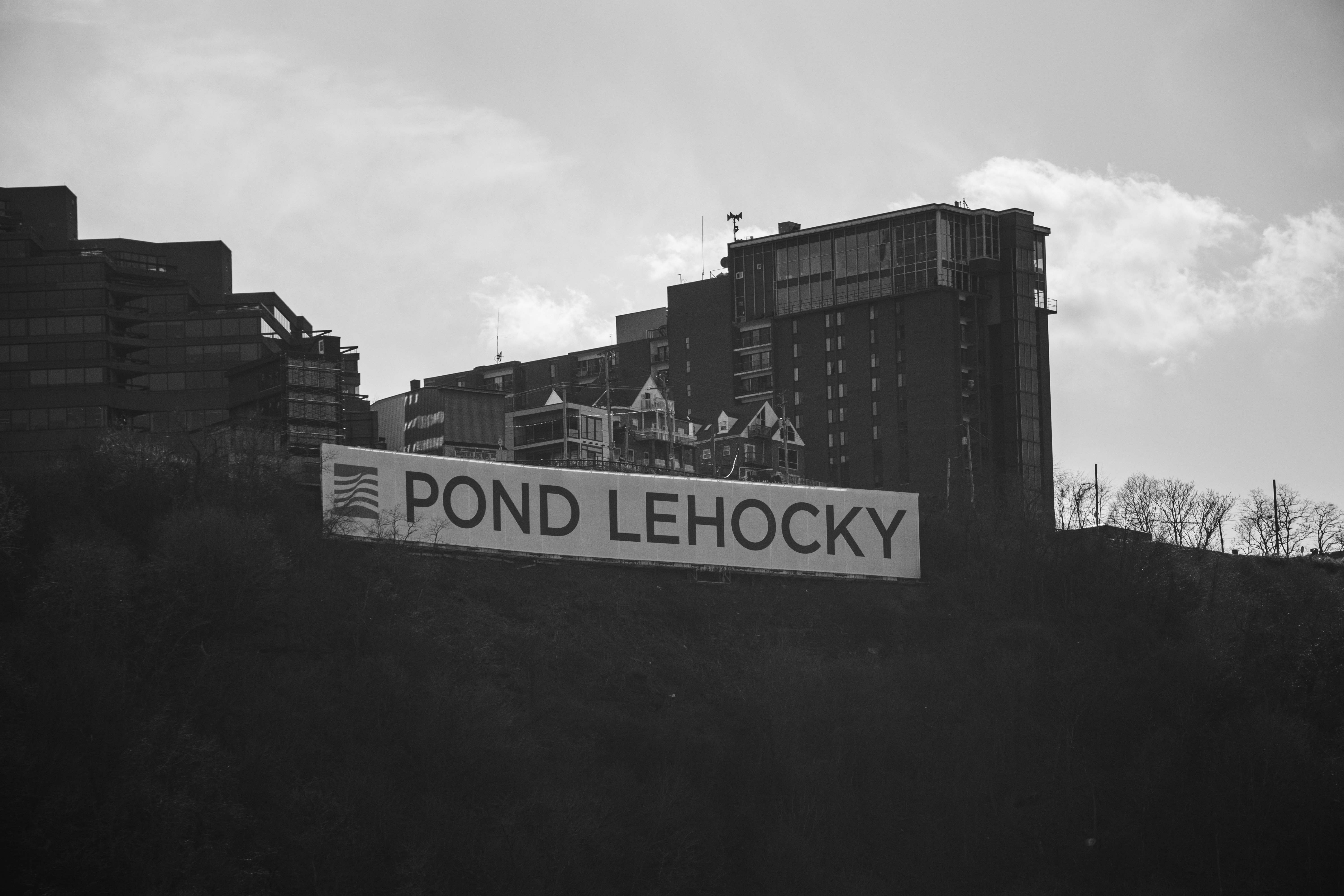 Black and white cityscape featuring a large sign with buildings silhouetted against a bright sky.