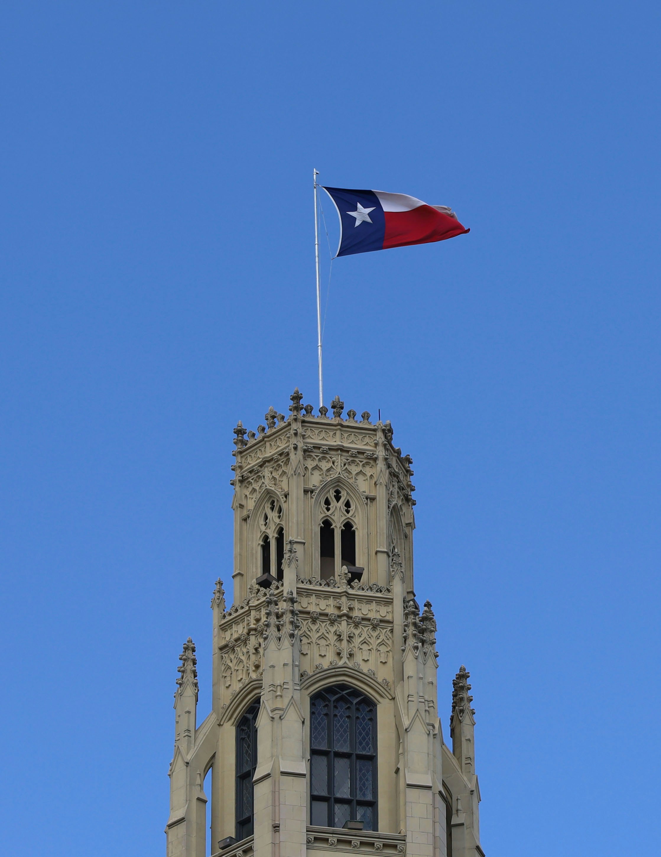 Flag over a Neo-Gothic Spire: Azure Sky and Intricate Stonework