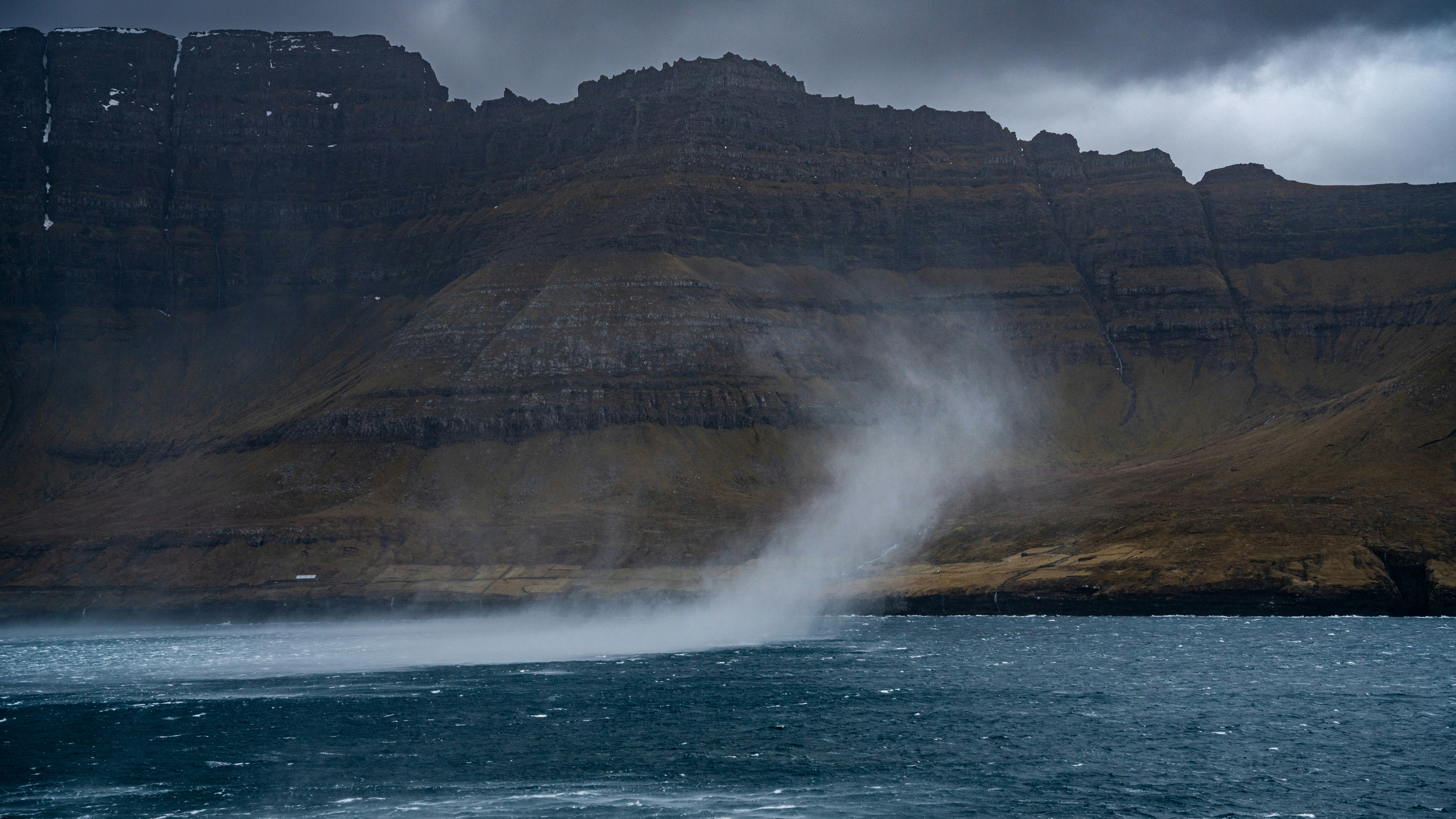 Spiral of Sea Mist Against Shadowed Cliffs