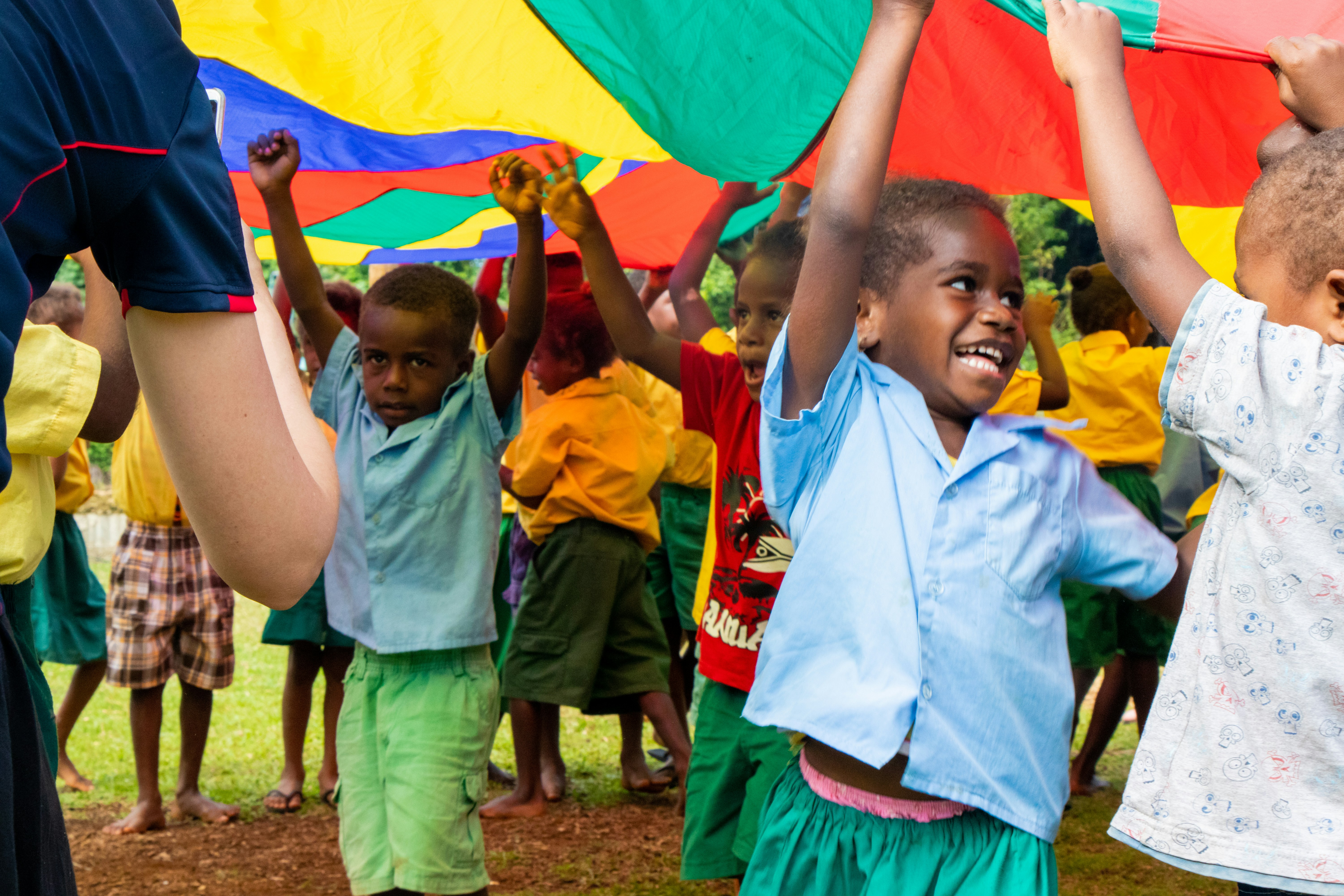 Children energetically lifting a colorful parachute in an outdoor setting.