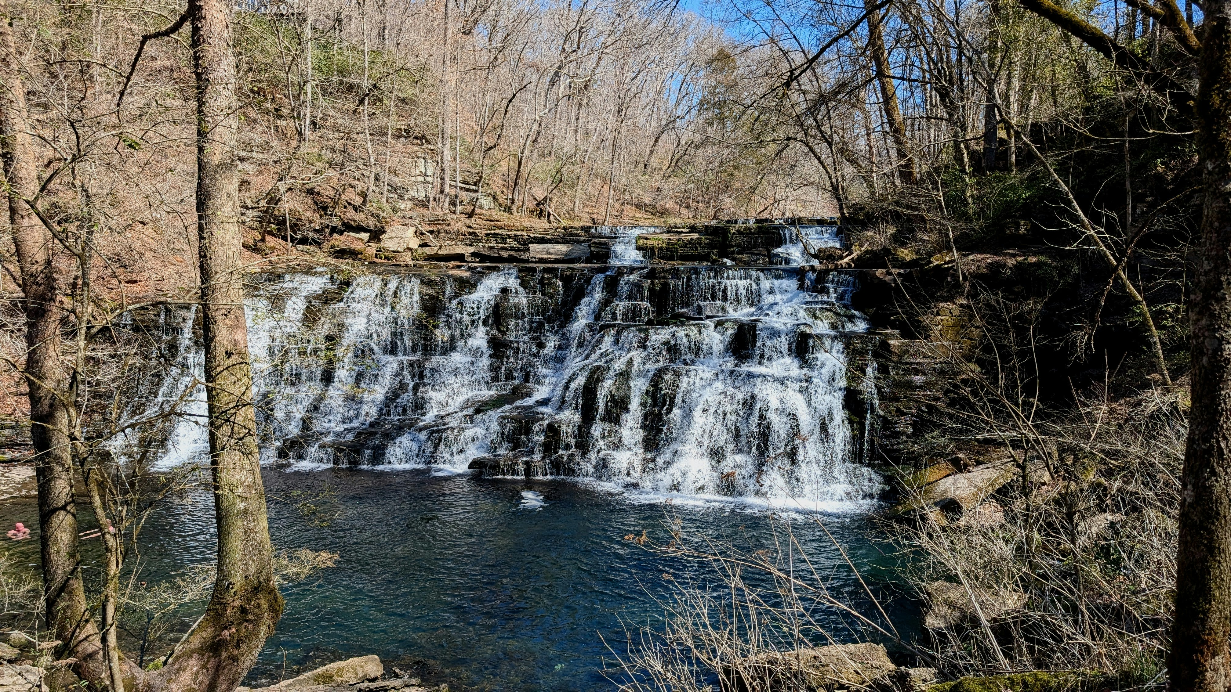 Waterfall flowing over rocky ledges surrounded by bare trees in a tranquil forest setting.