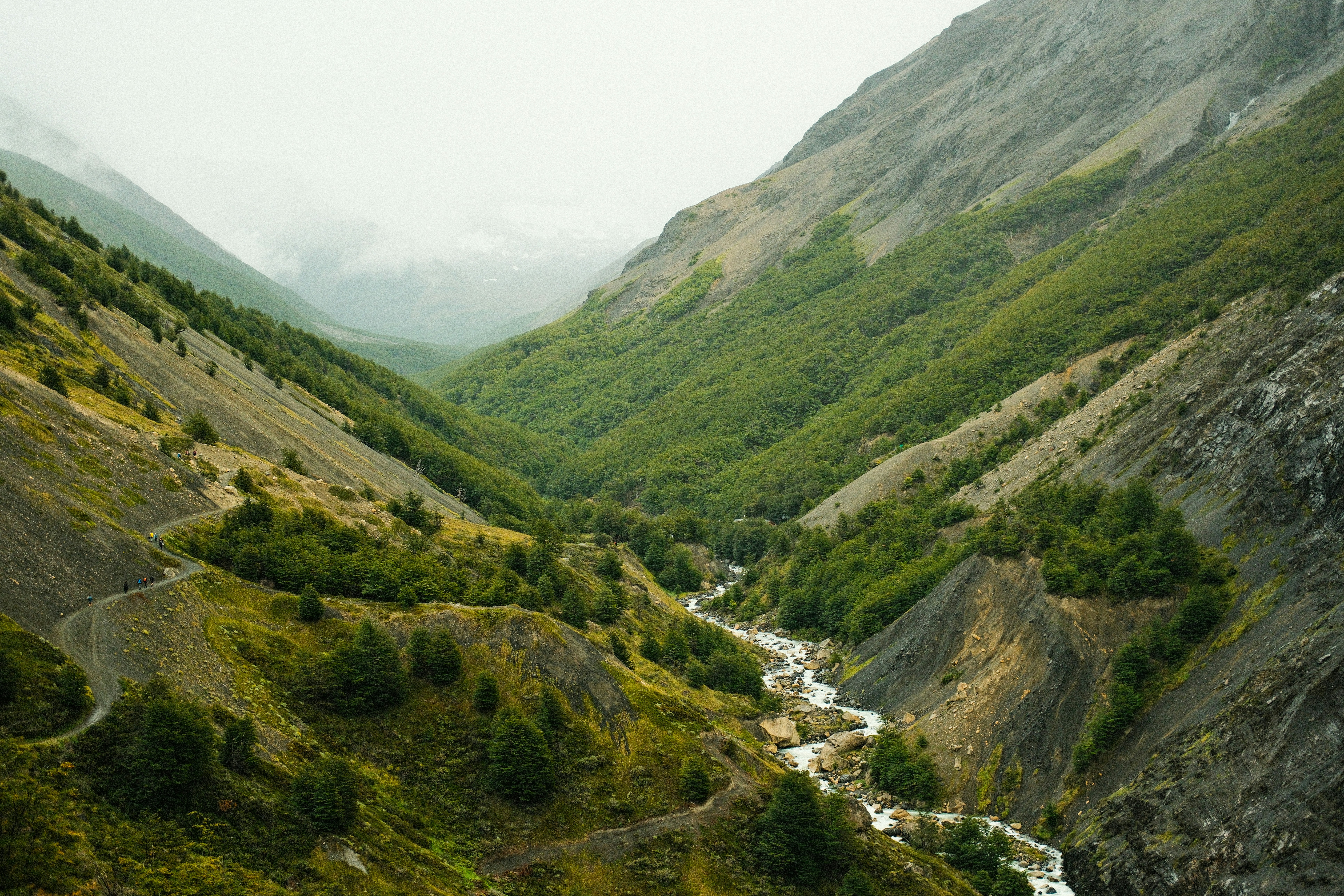 Lush green valley with a winding stream framed by rugged mountains under an overcast sky.