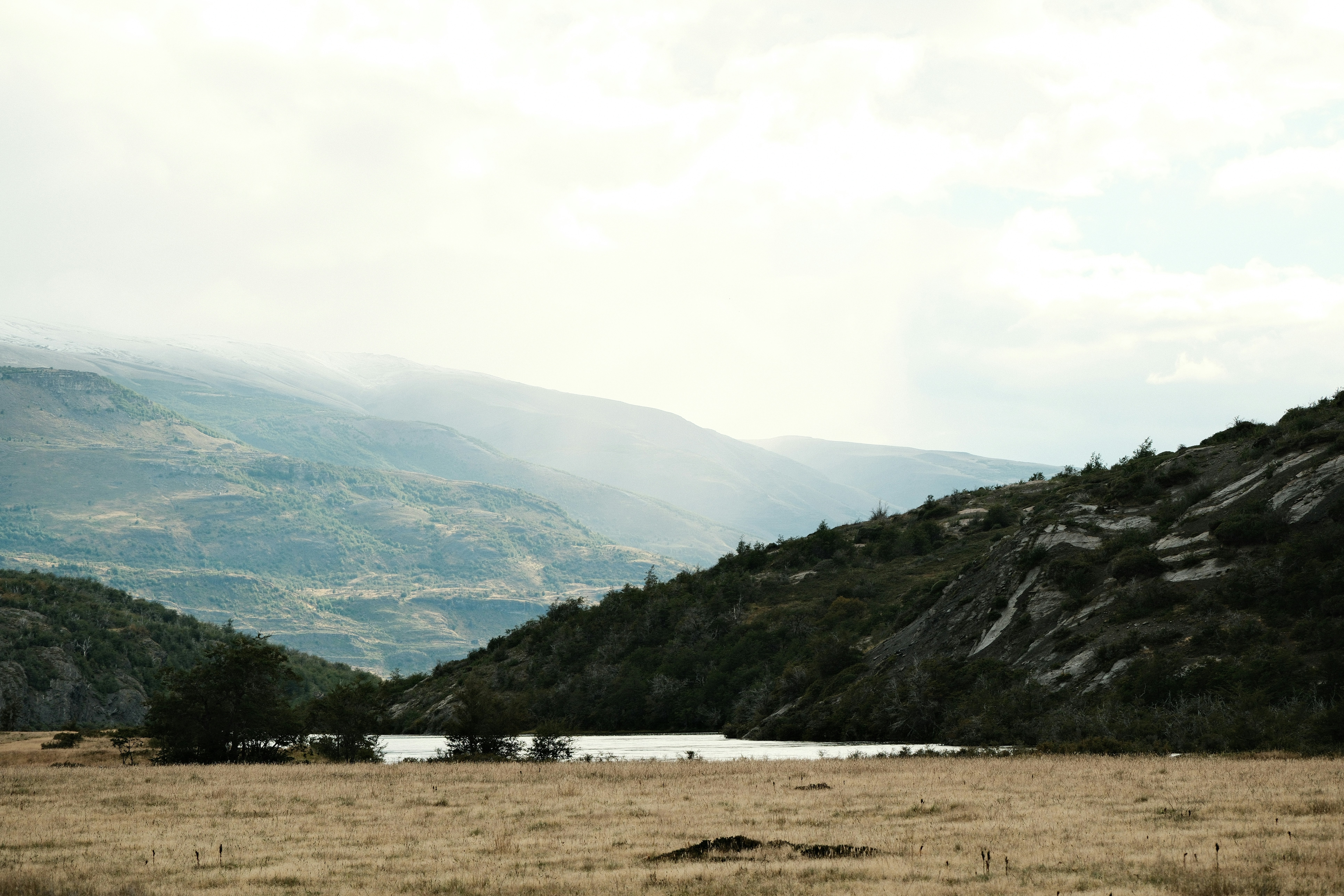 Valley Verge: Golden Grass Meets a Ribbon of Water Beneath Distant Ridges